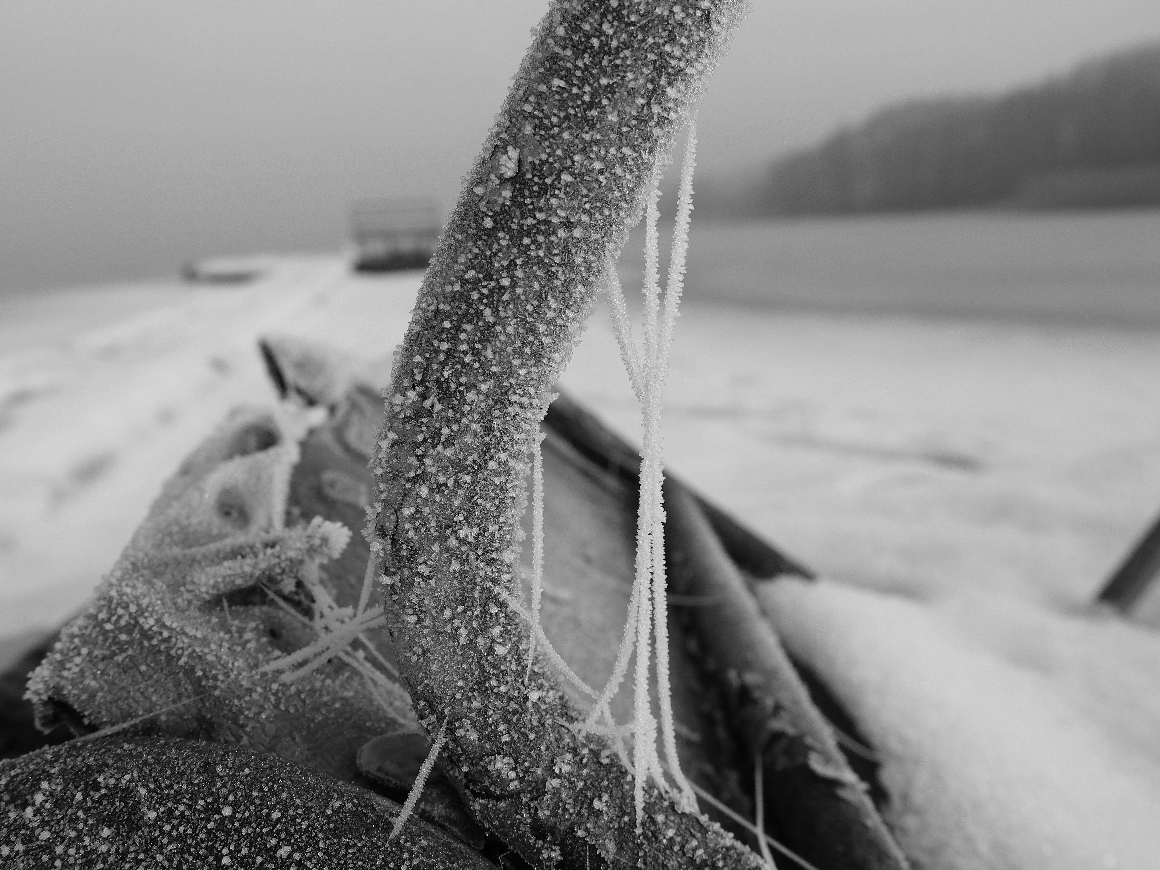 Frost-covered ropes and chains on a snow-laden beach with a foggy riverbank in the background.