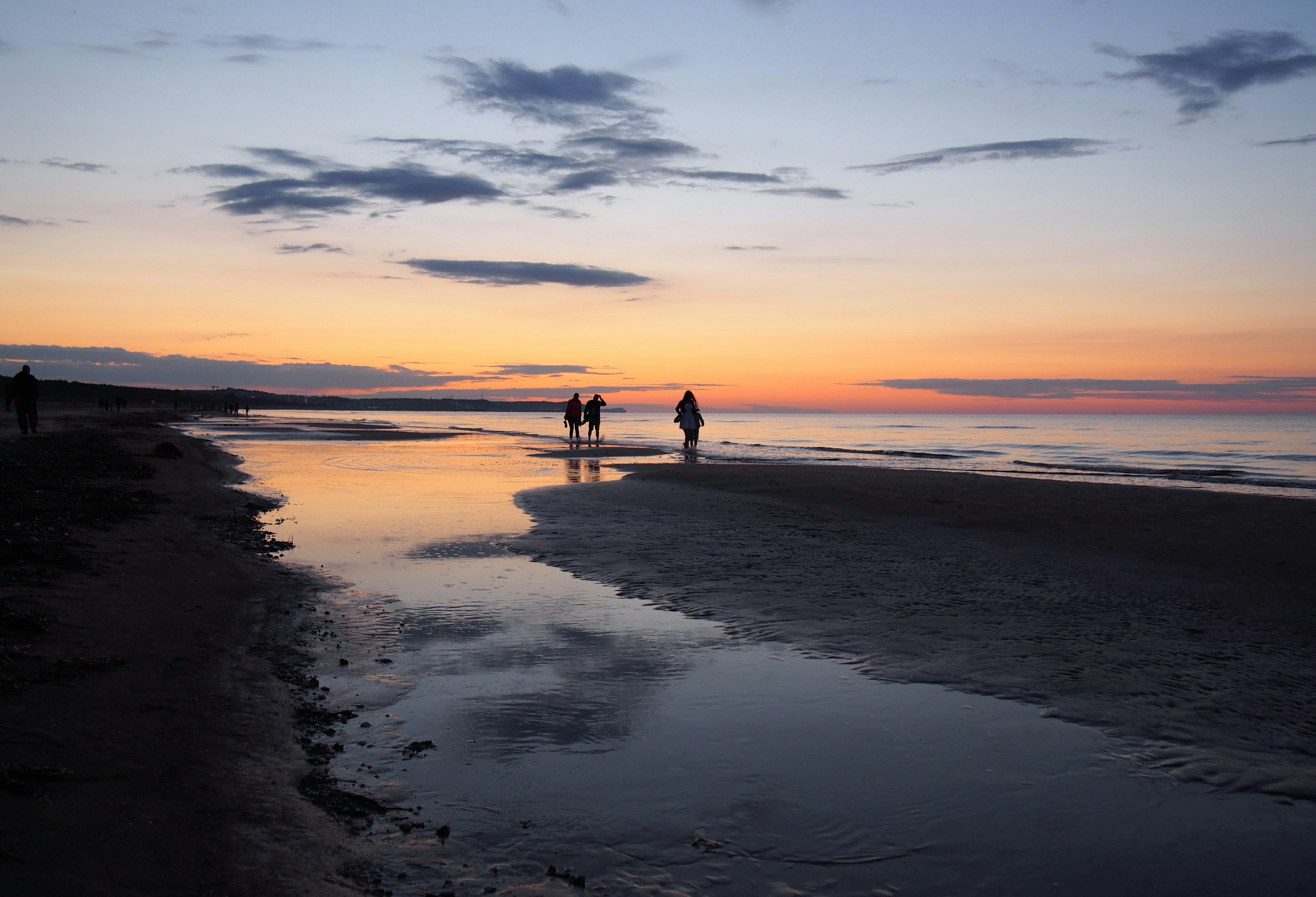 Silhouetted figures walk along a tranquil beach at sunset with vivid hues reflecting in the water.