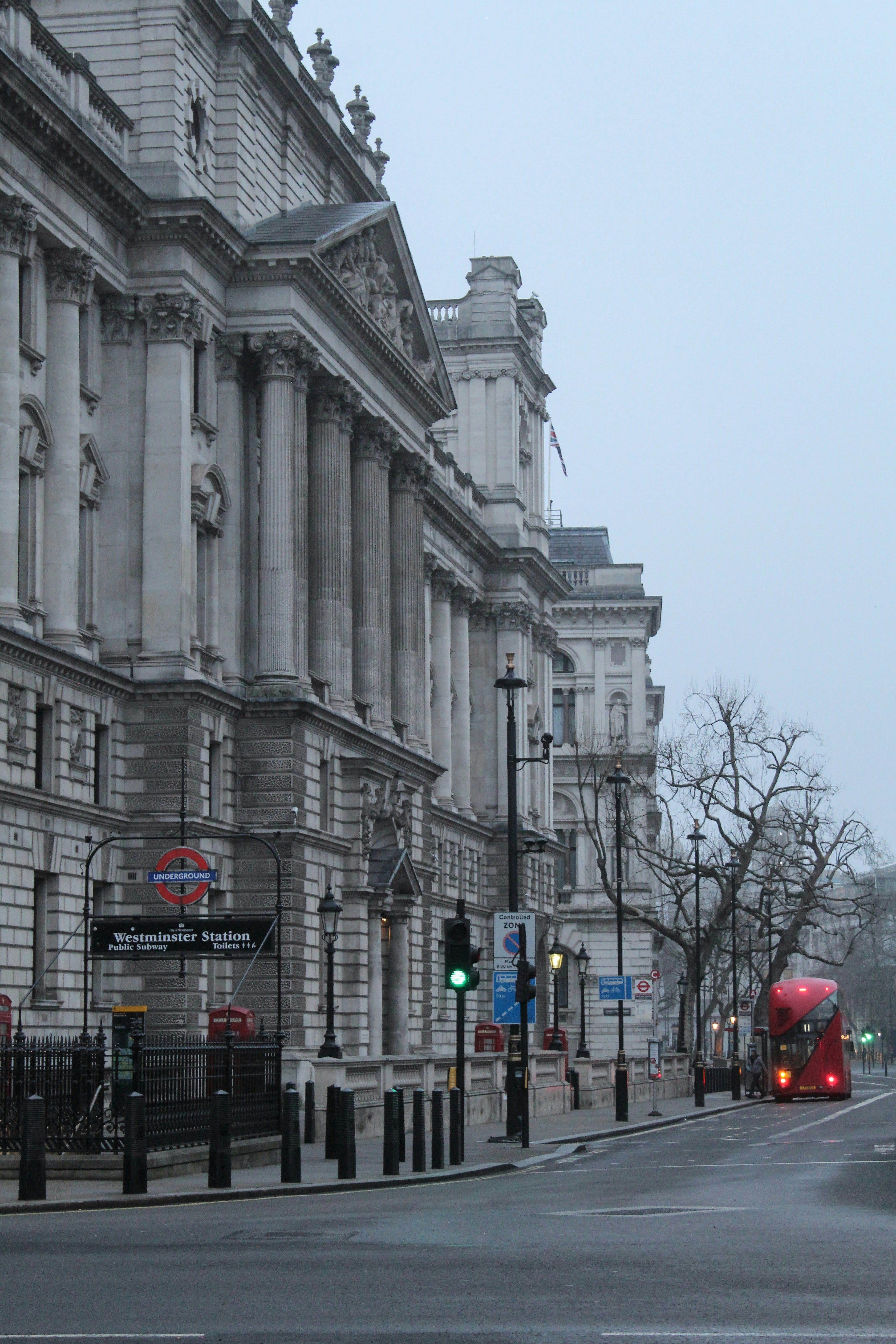 Historic Westminster Station sign framed by classic architecture, with a red double-decker bus turning down a foggy street.