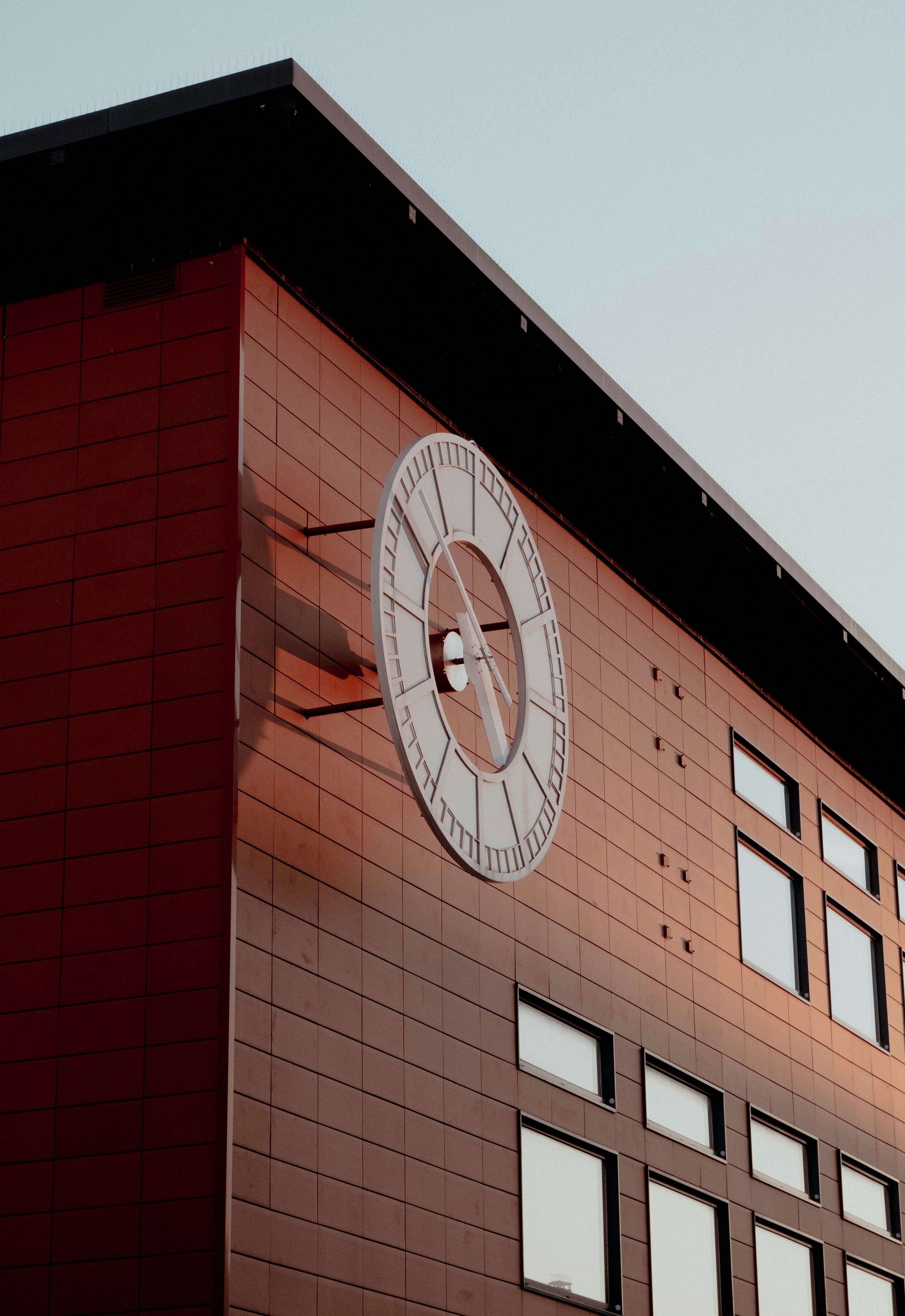 A modern building facade featuring a prominent clock design, reflecting the soft hues of the sky. The interplay of light and shadow enhances the architectural details.