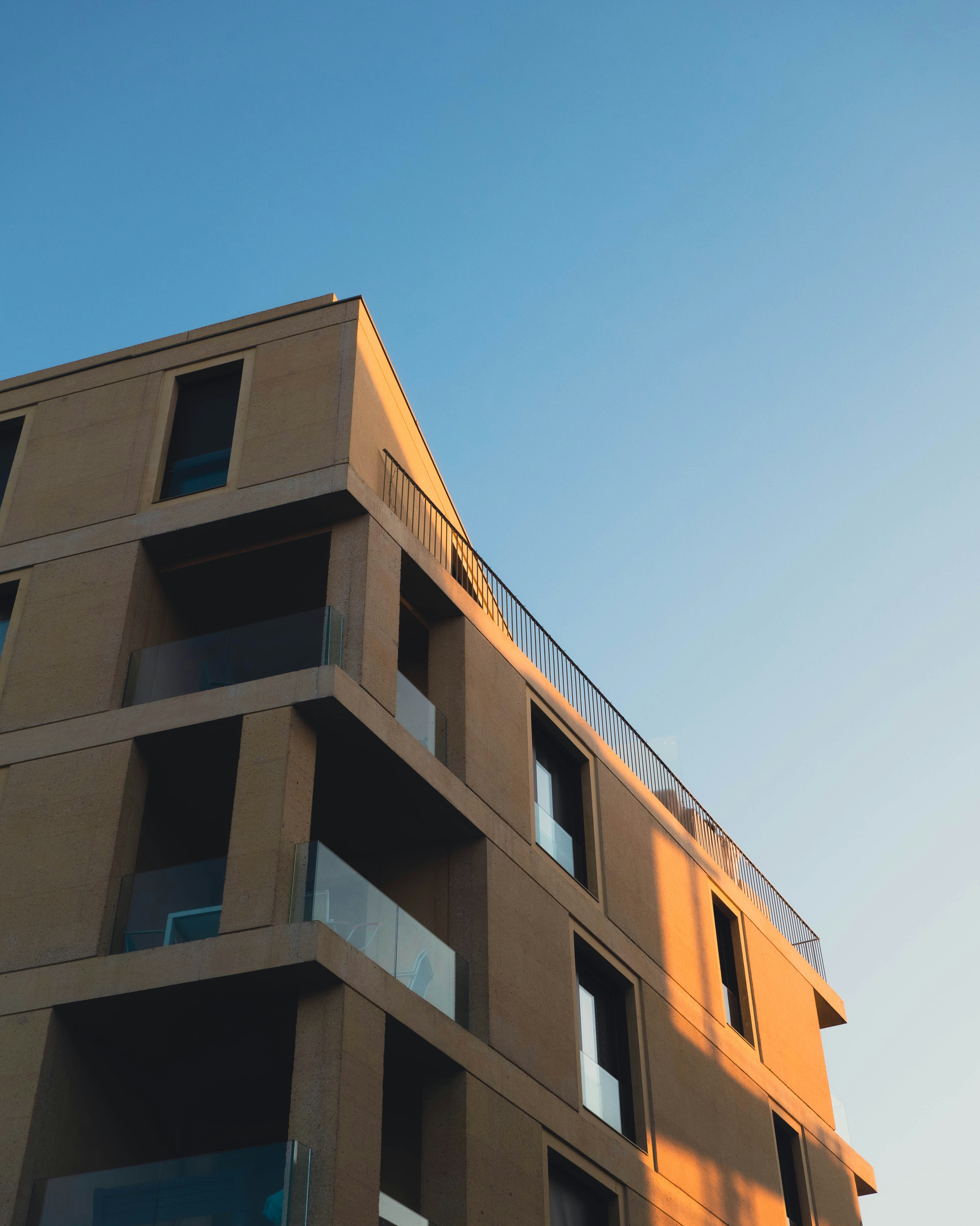 Contemporary building with angular design and glass balconies, illuminated by soft evening light against a clear blue sky.