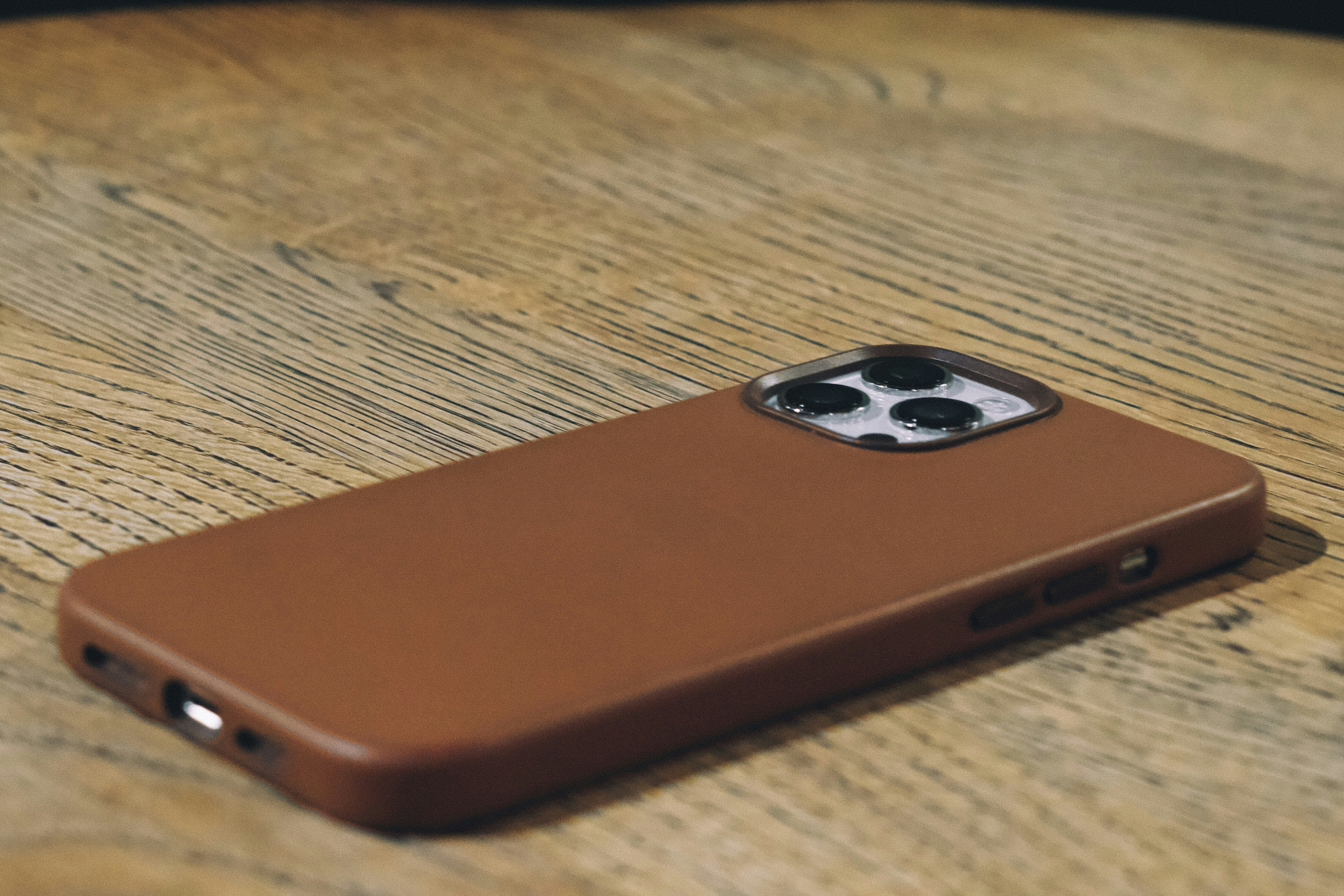 Brown leather iPhone case resting on a wooden surface under warm light