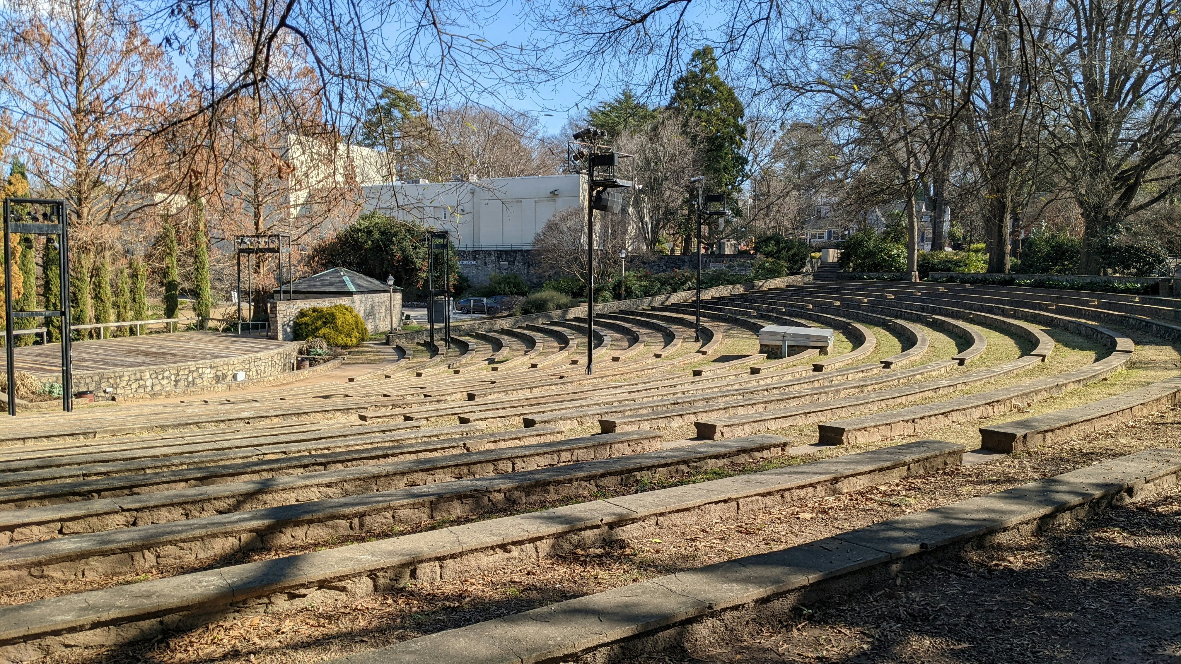 Outdoor amphitheater with curved wooden seating under a clear blue sky, surrounded by leafless trees.