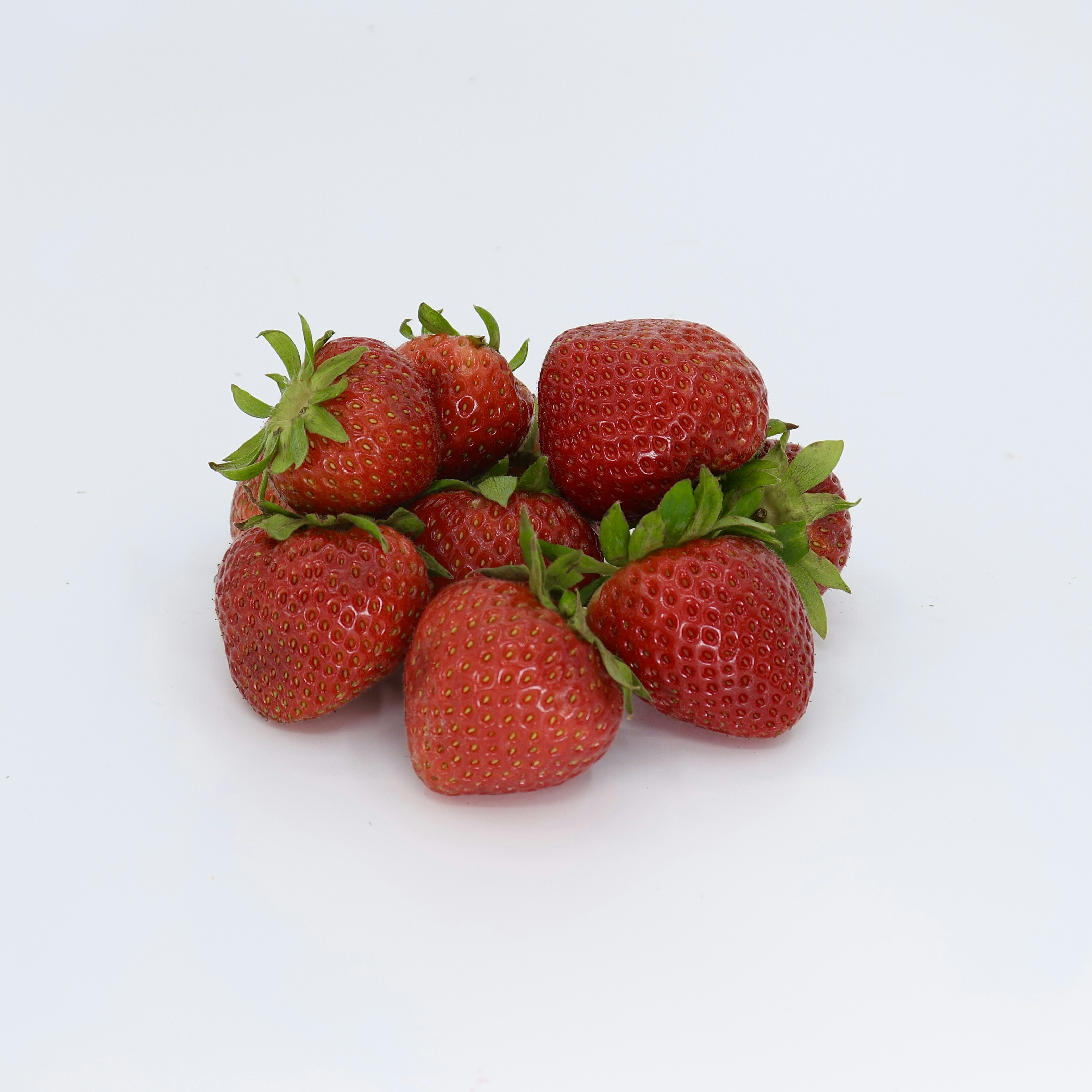 Vibrant cluster of fresh strawberries with lush green leaves against a pristine white background.