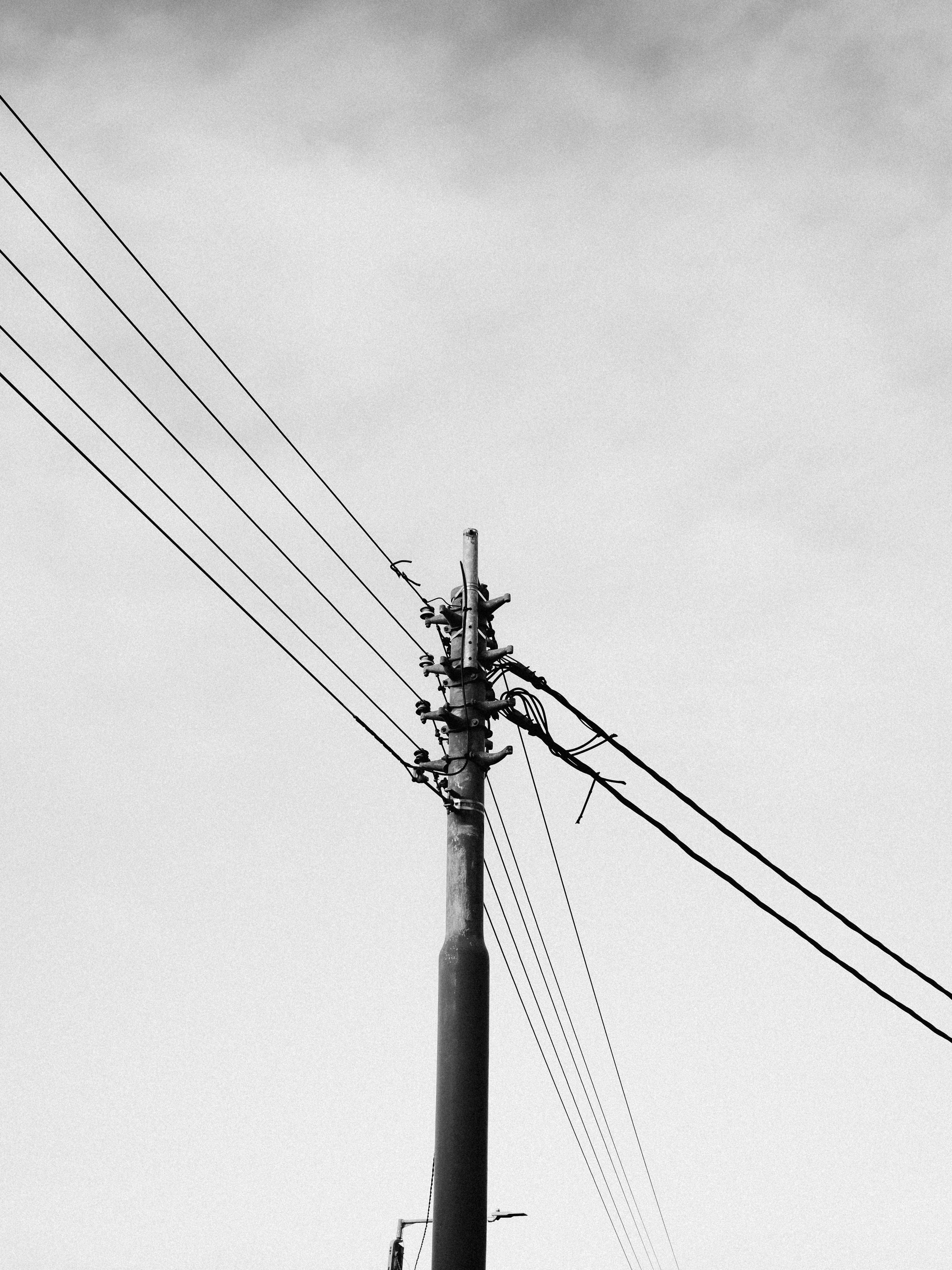 Black and white photograph of a utility pole with power lines stretching across a cloudy sky.