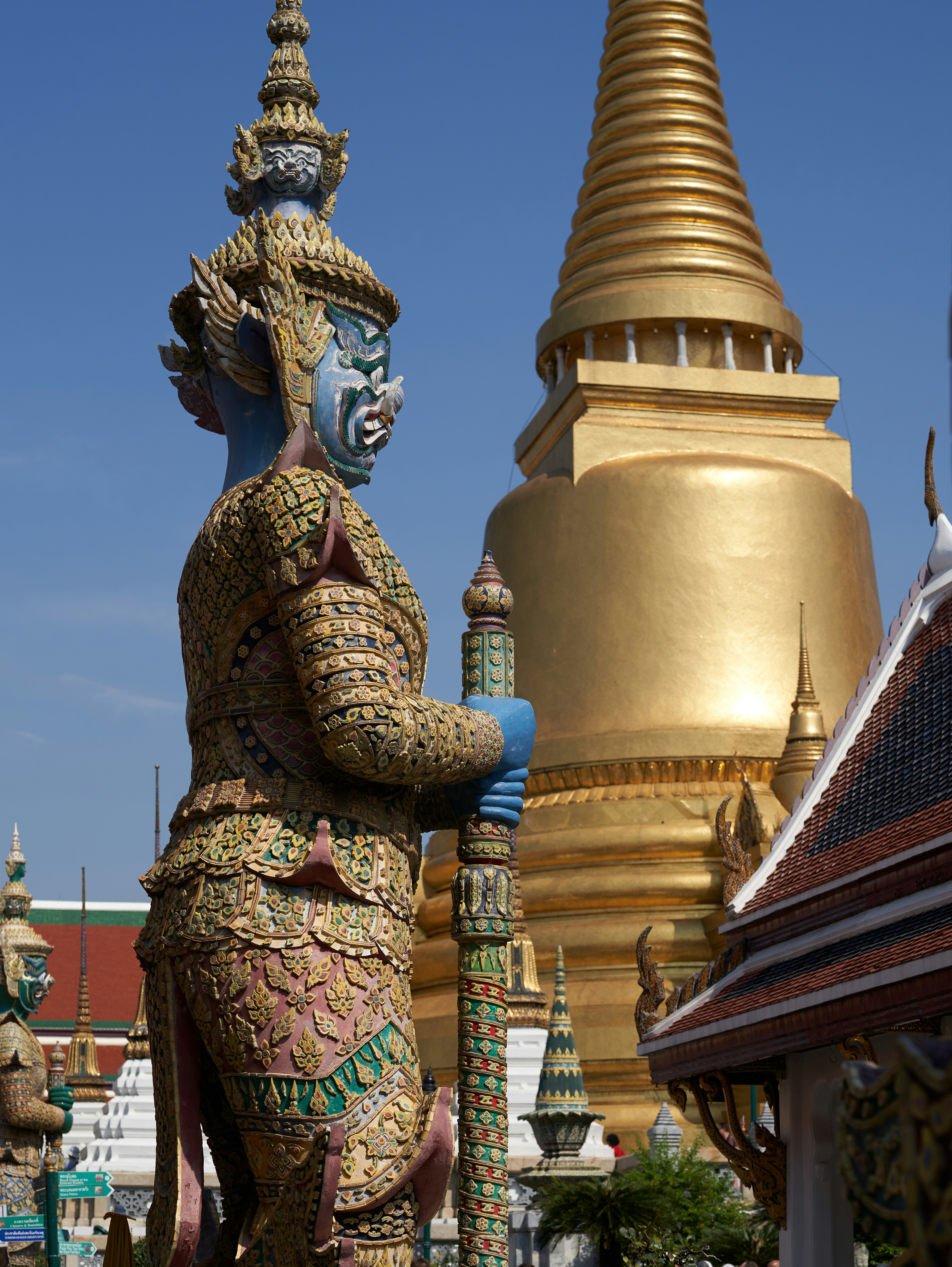 Majestic statue adorned in intricate details stands guard beside a gleaming golden stupa, showcasing the rich cultural heritage of the temple complex.