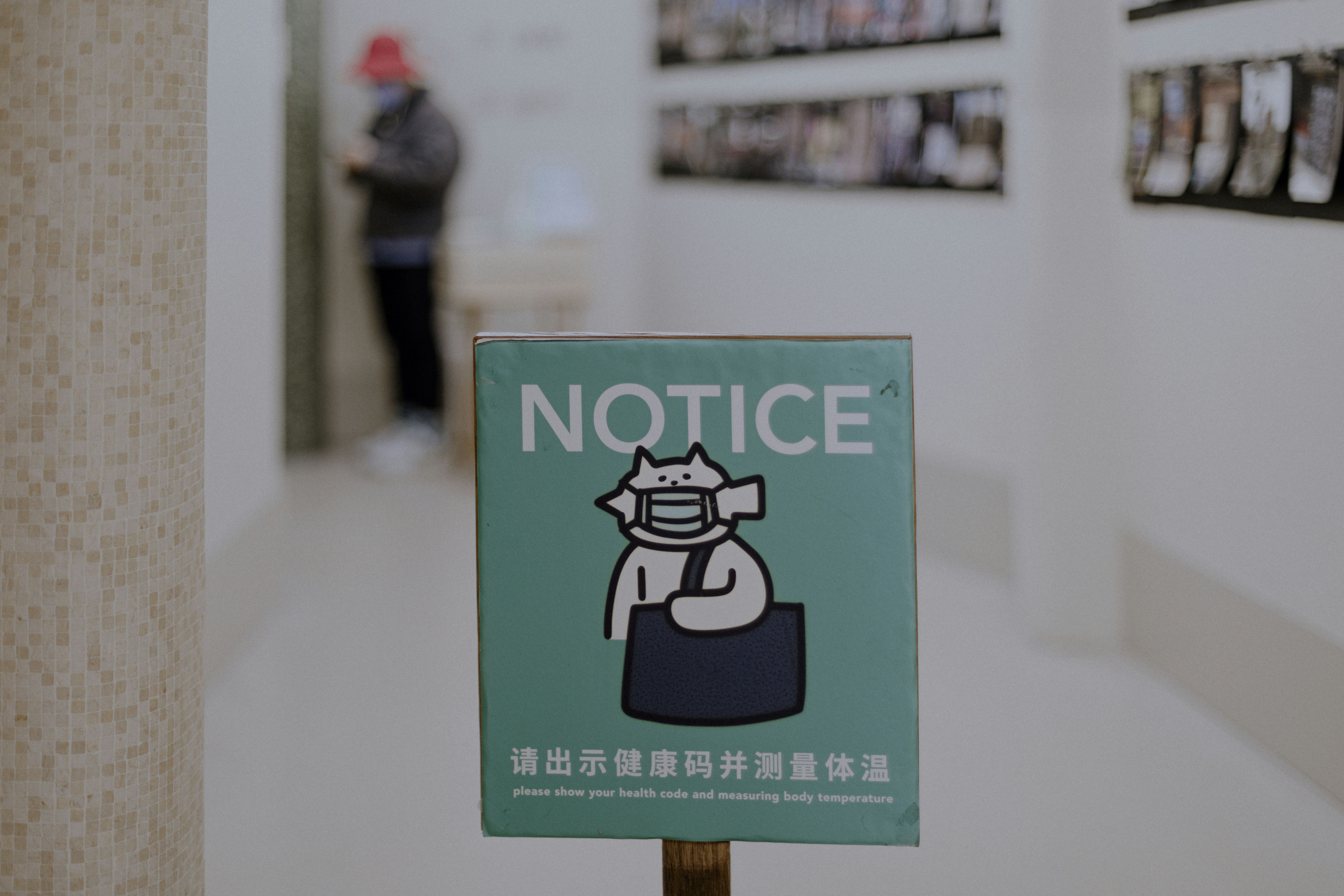 Sign reminding visitors to show health codes and undergo body temperature checks, featuring a cartoon character wearing a mask. 