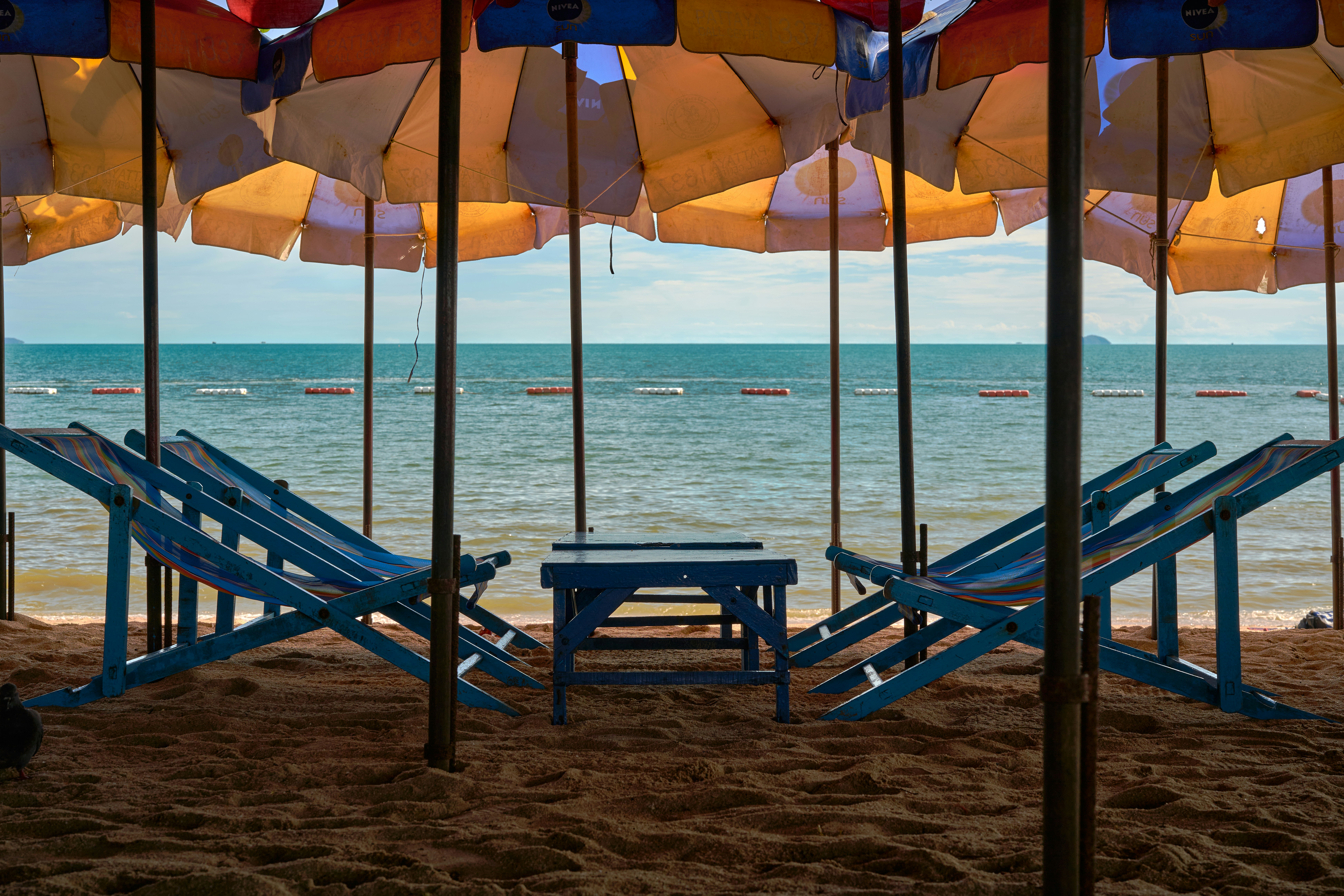 Colorful beach umbrellas create a vibrant canopy over empty lounge chairs, framing a tranquil view of the ocean. The scene invites relaxation and escape.