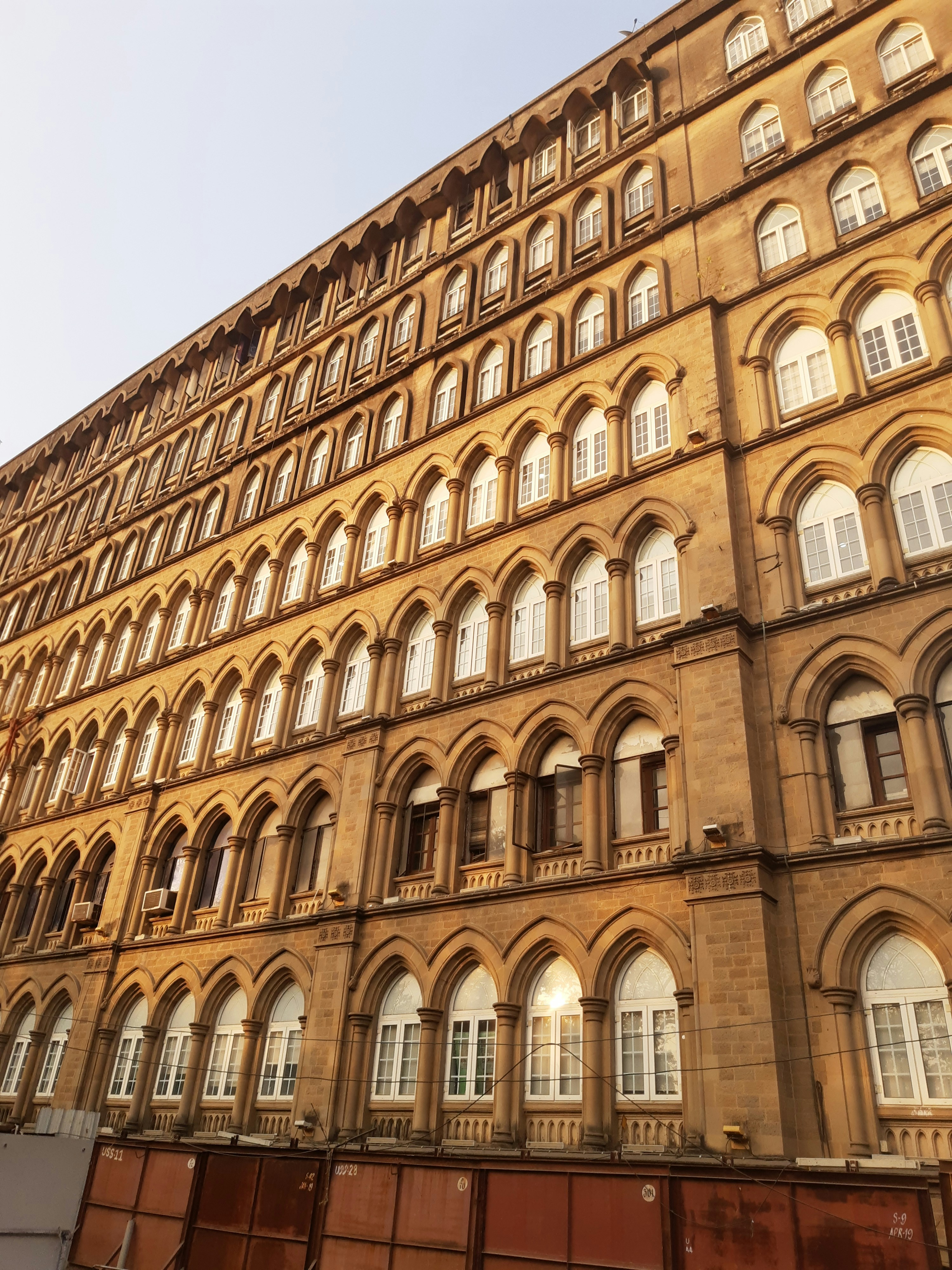 Historic building facade featuring a series of elegant arches and windows, bathed in warm sunlight.