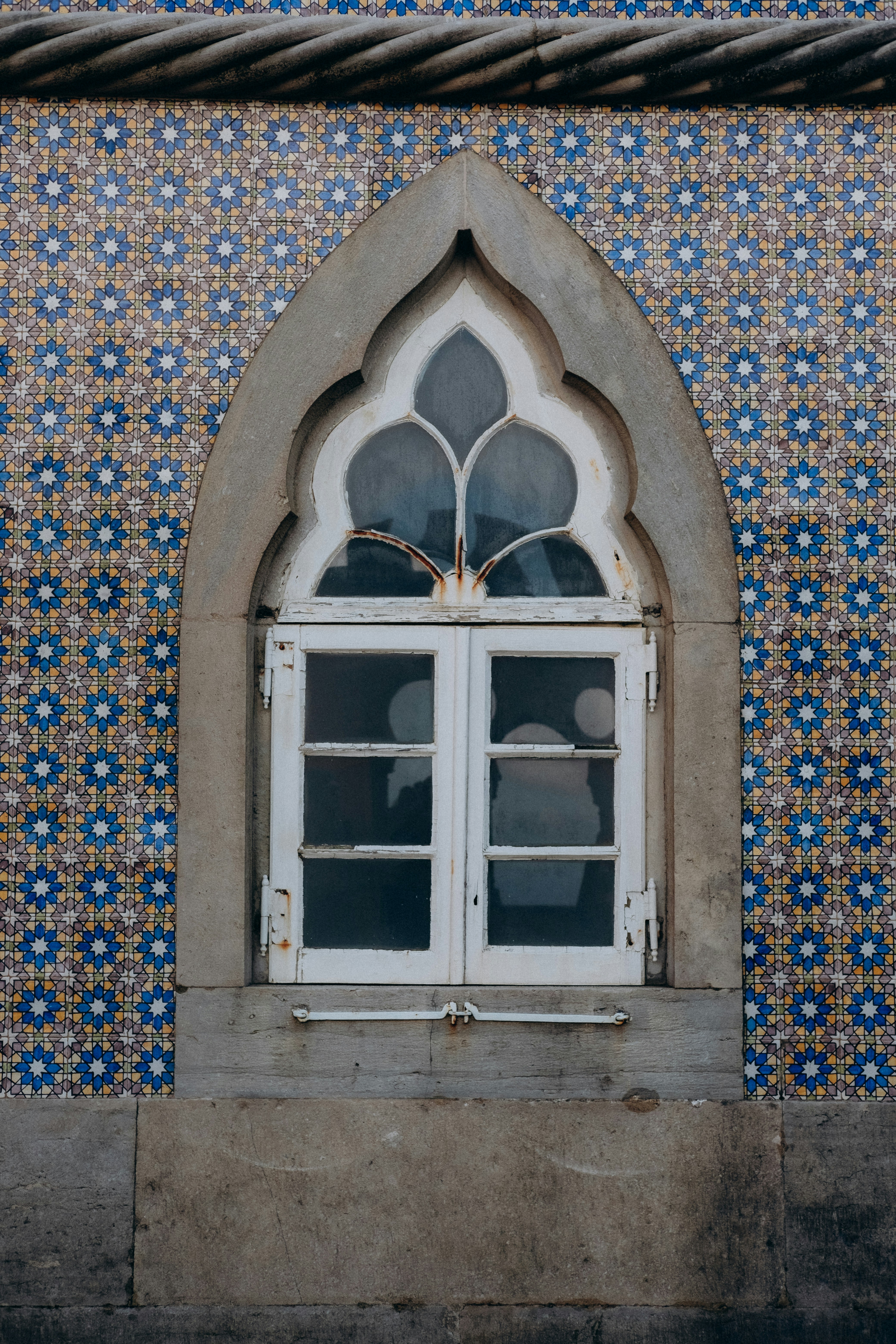 Intricately designed window set against a vibrant tiled wall, showcasing a blend of architectural styles. The ornate details highlight cultural artistry.