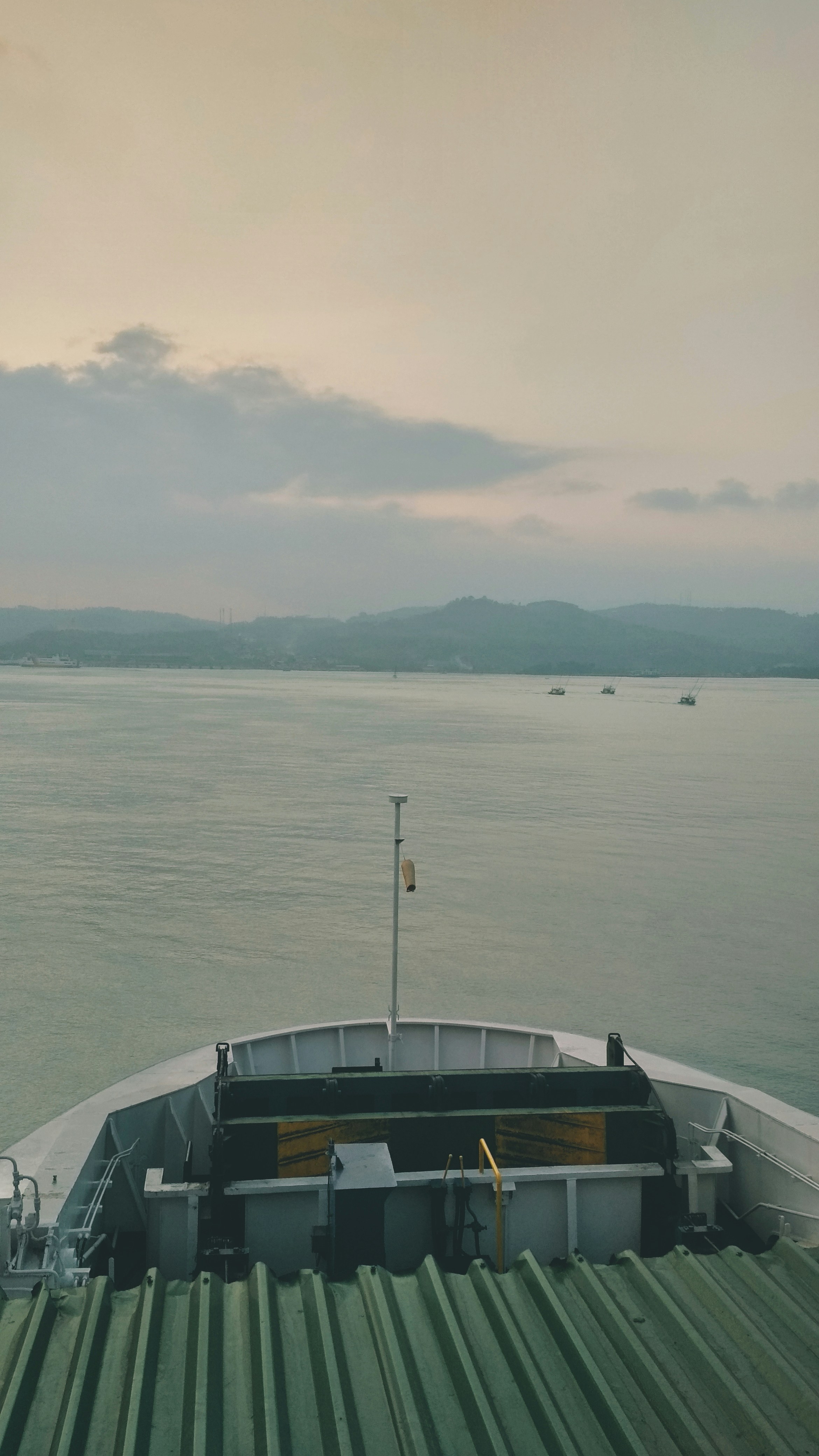 View from the bow of a boat overlooking calm waters and distant hills under a soft morning sky.