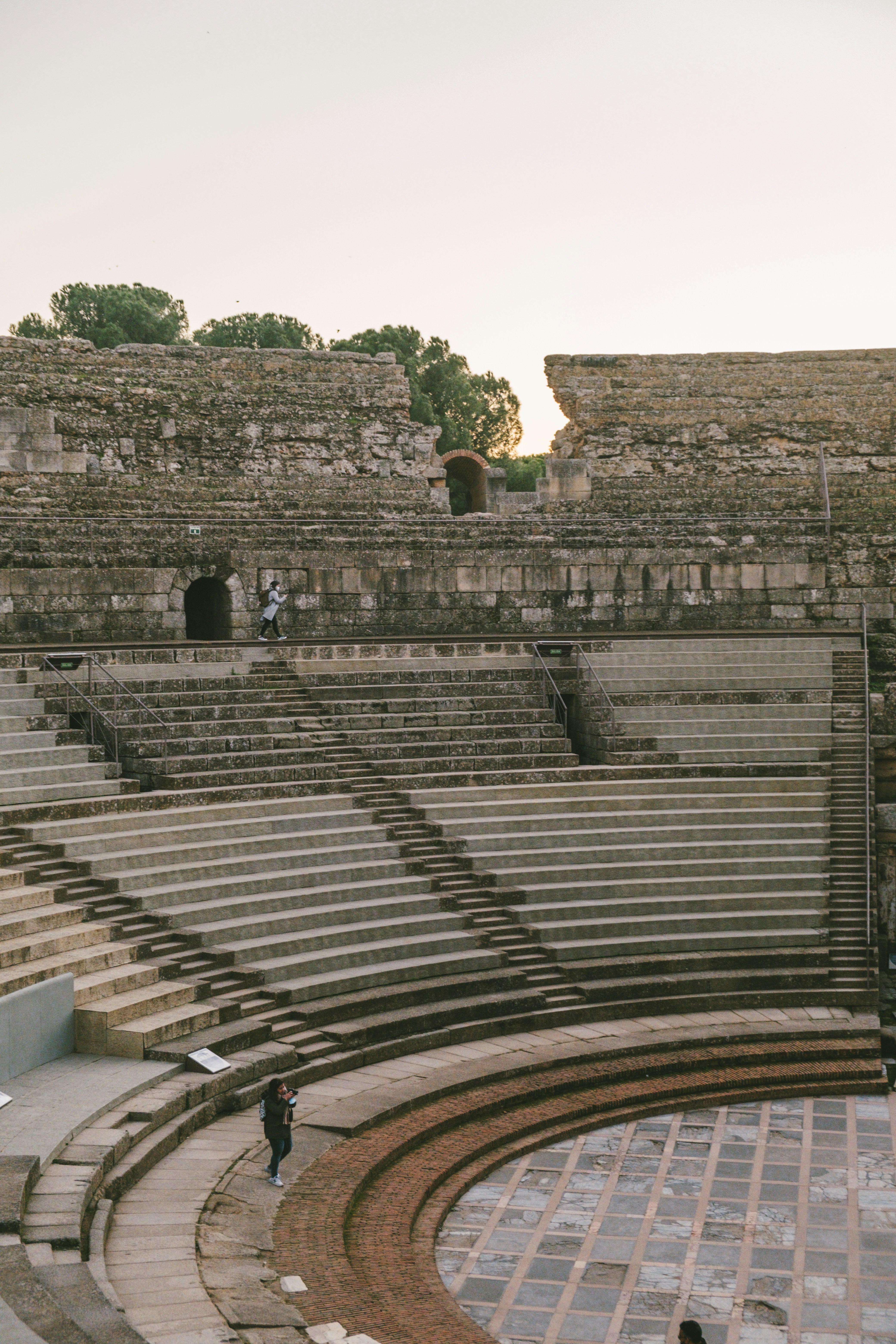 Ruins of an ancient amphitheater, showcasing tiered seating and stone architecture under a soft twilight sky.