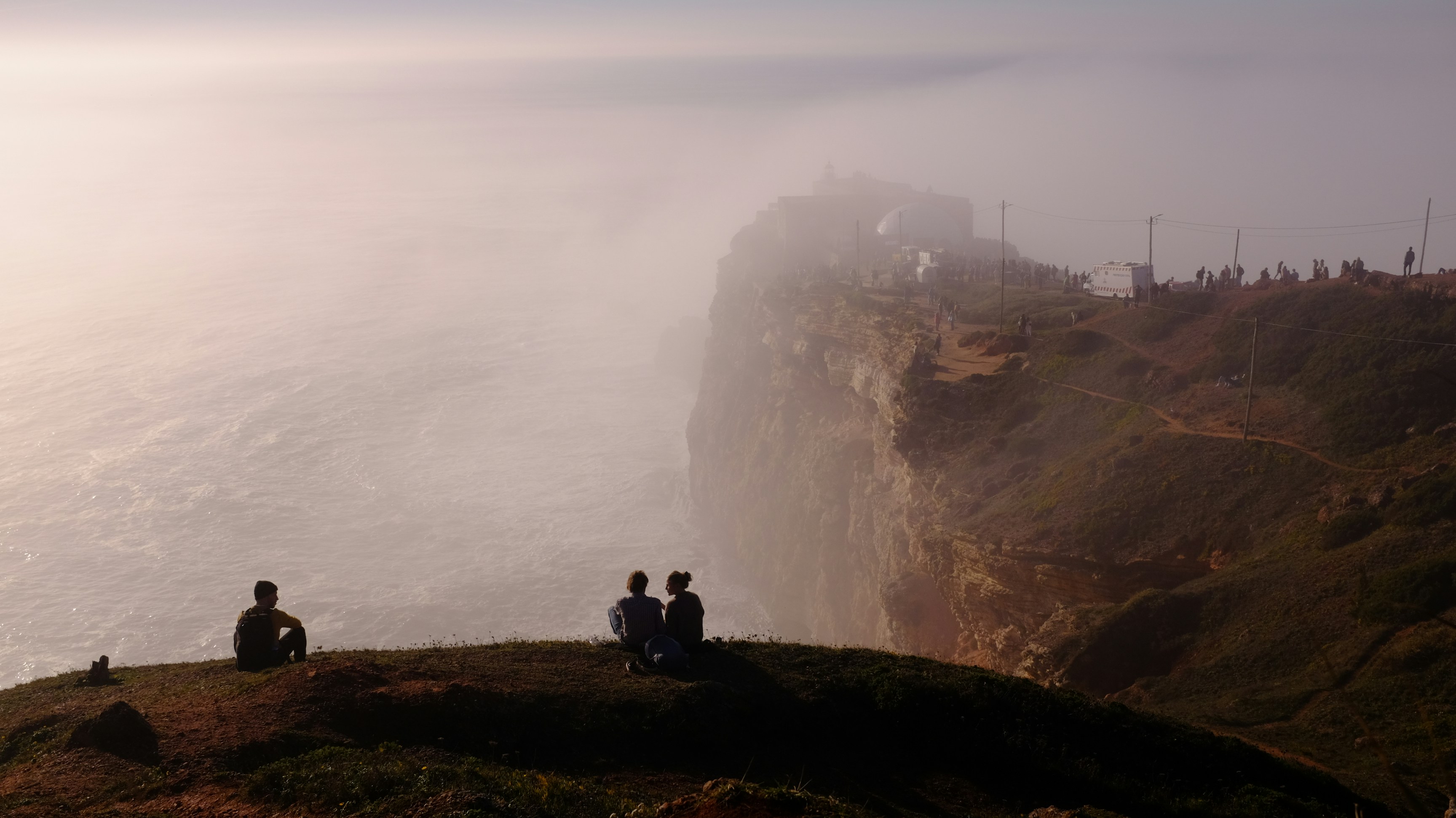 Three people sitting on a cliff overlooking the ocean photo – Free ...