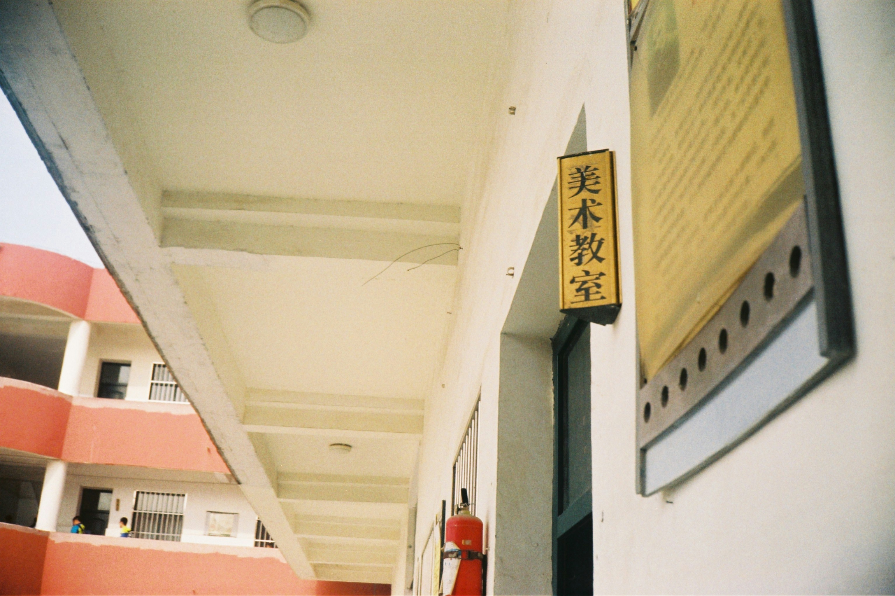Signage for an art classroom under a covered walkway, framed by architectural elements of a building. A fire extinguisher is visible nearby.