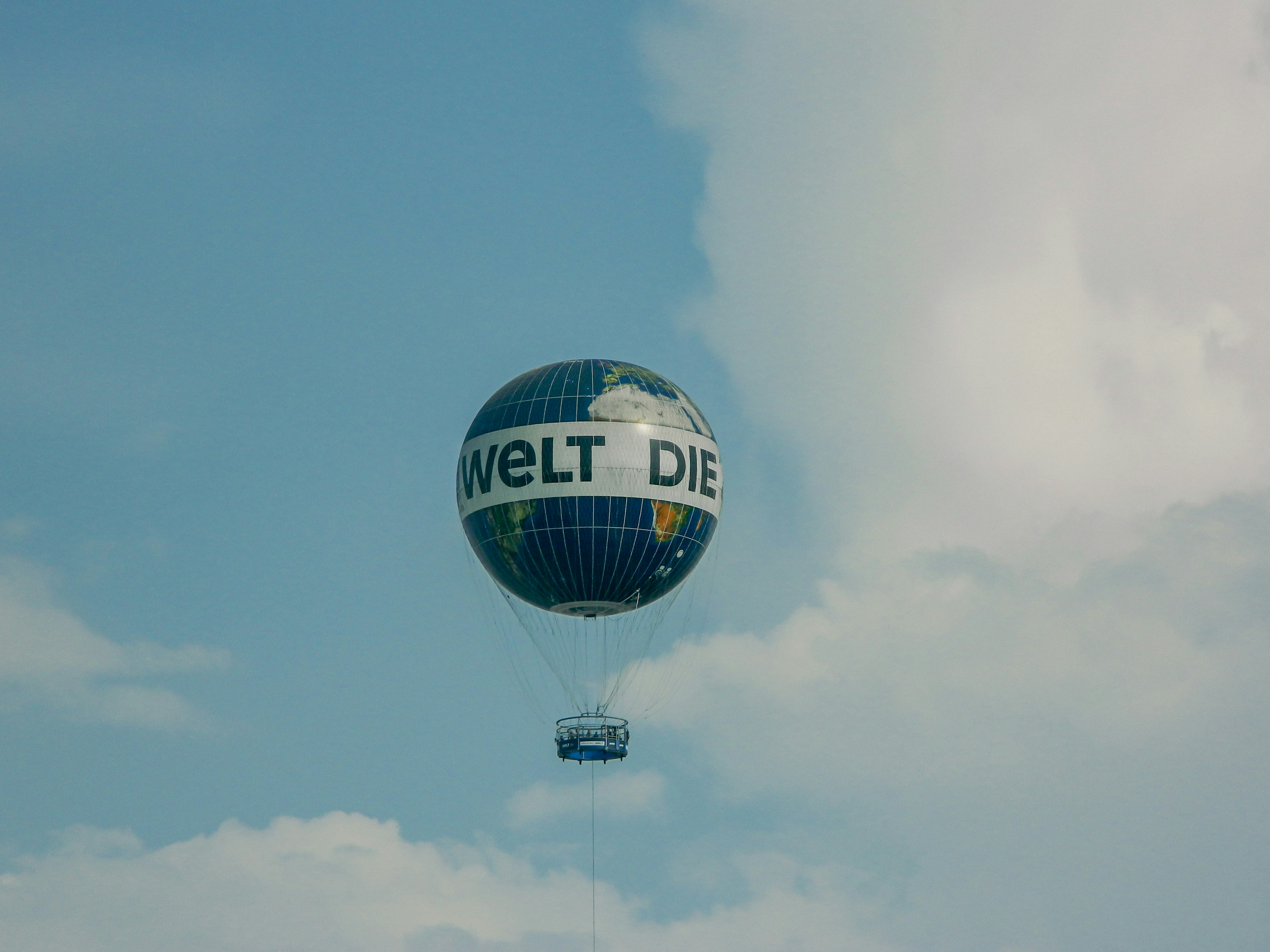 A vibrant hot air balloon displaying the word 'WELT' against a backdrop of fluffy clouds.