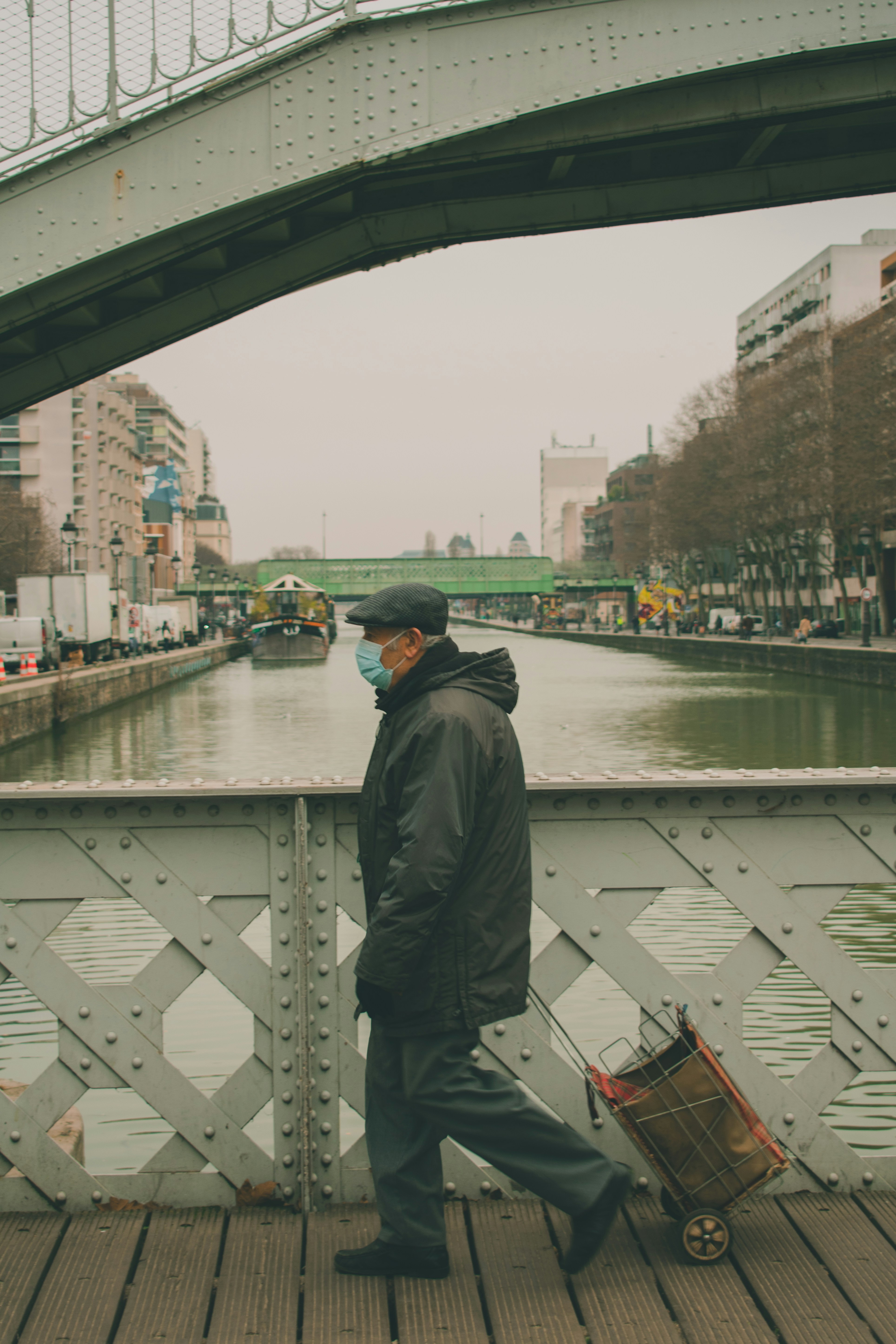 A man walking across a bridge while wearing a face mask photo – Free ...