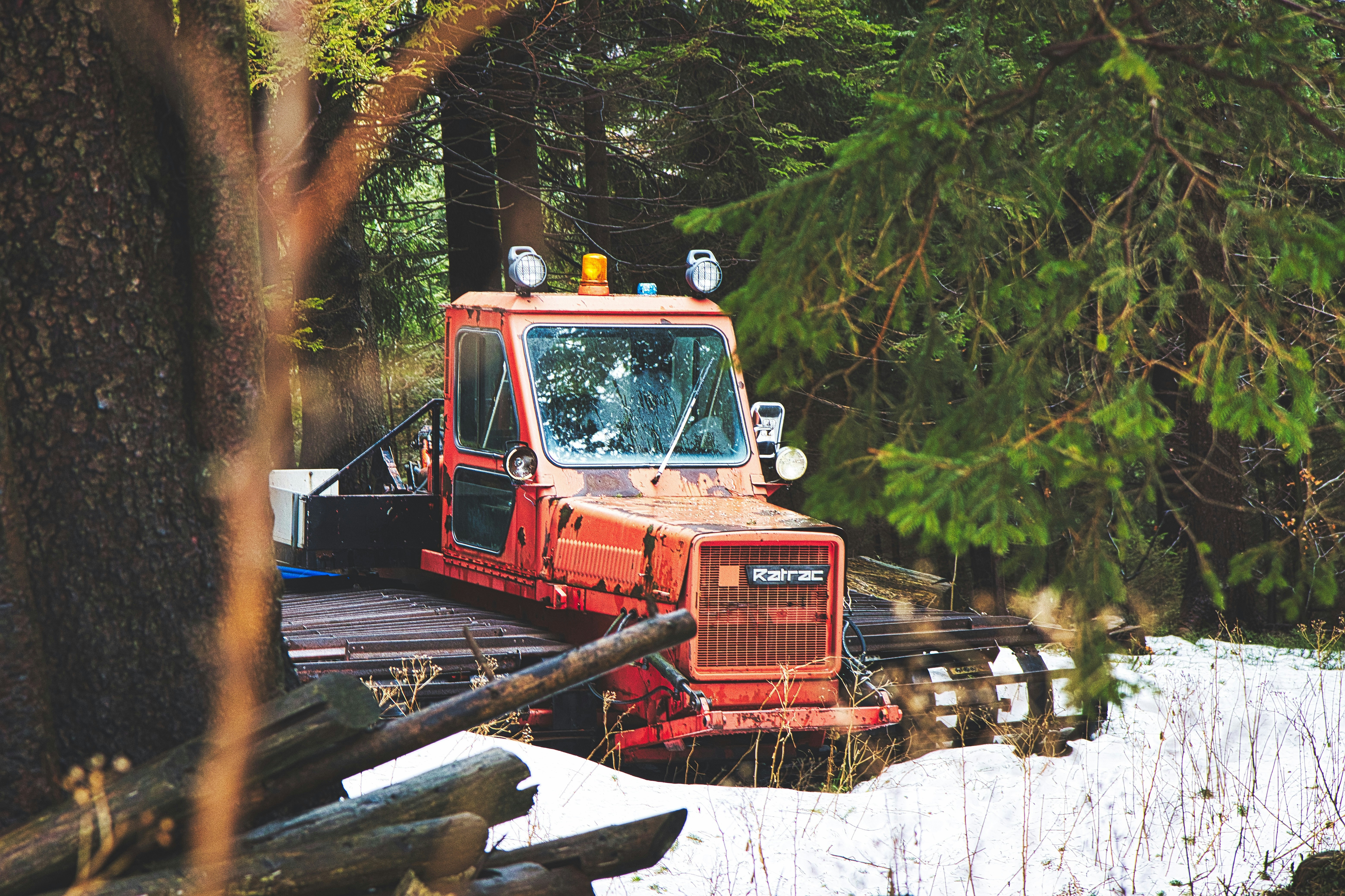 An old red snowplow partially obscured by trees and snow, highlighting the passage of time in a forest setting.