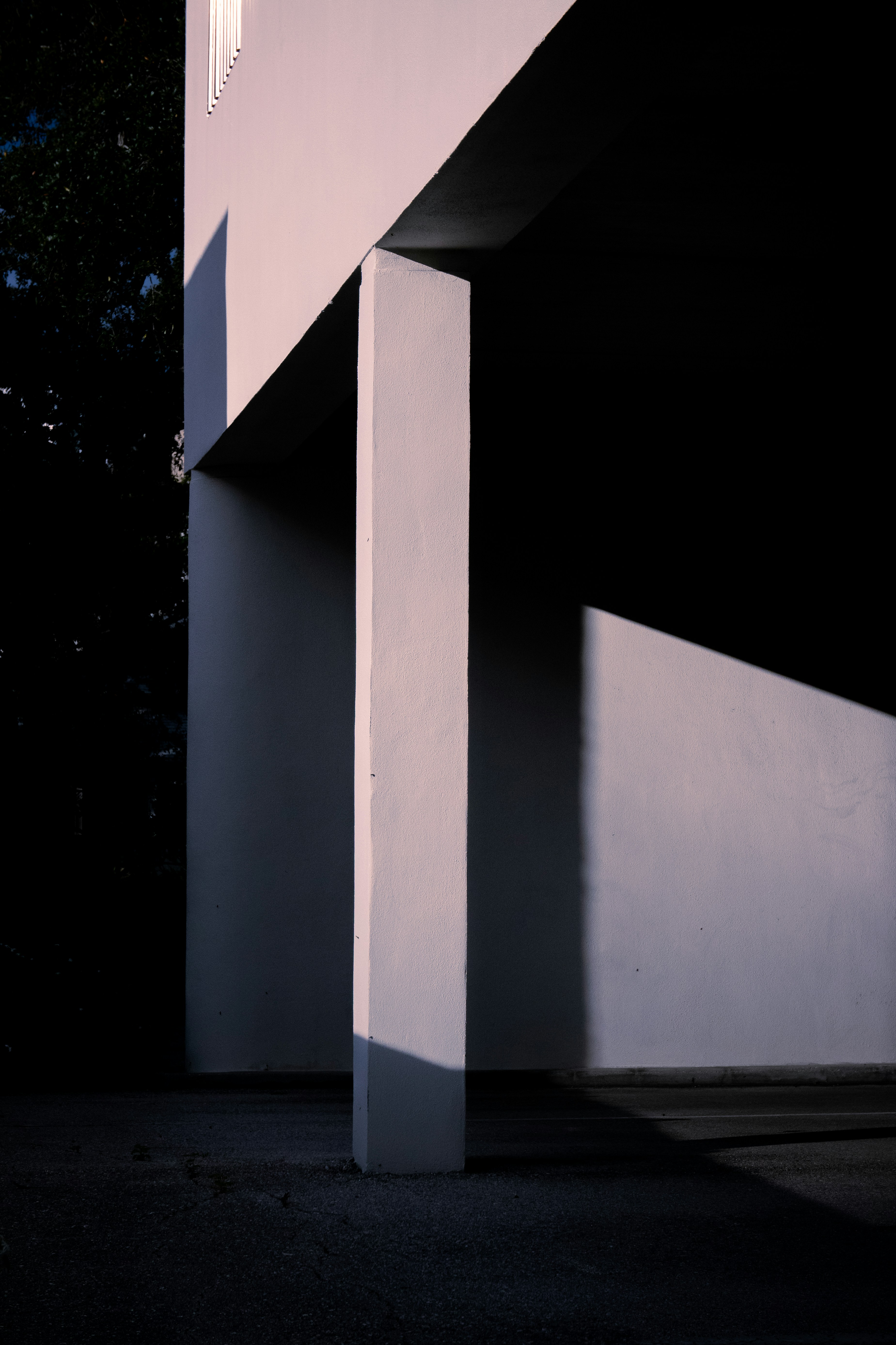 A tall, minimalist column casts a dramatic shadow against a smooth wall, highlighting the interplay of light and architectural elements.