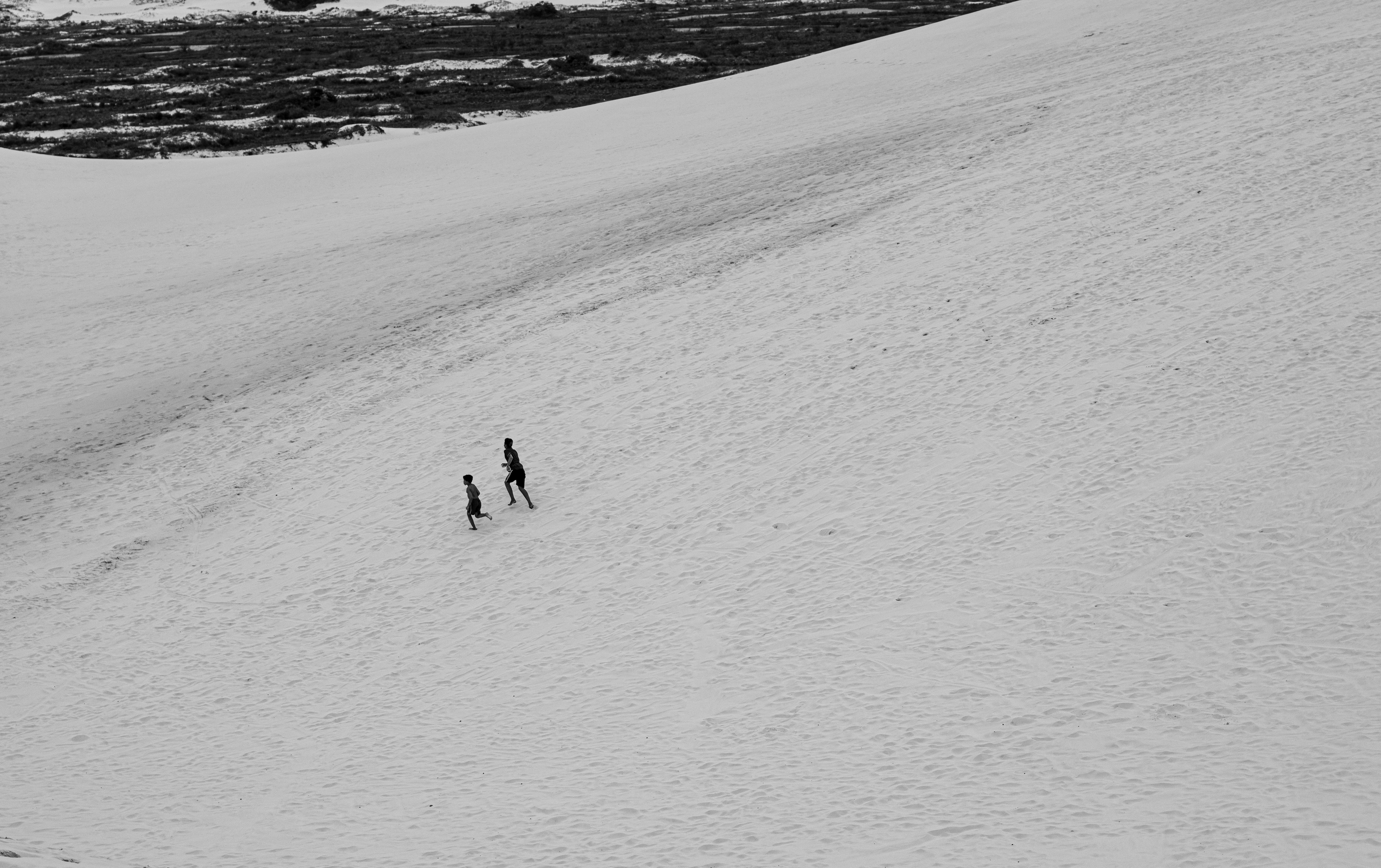 Two figures traverse a vast, snowy landscape, their footprints marking the untouched terrain. The scene captures the essence of exploration and solitude.