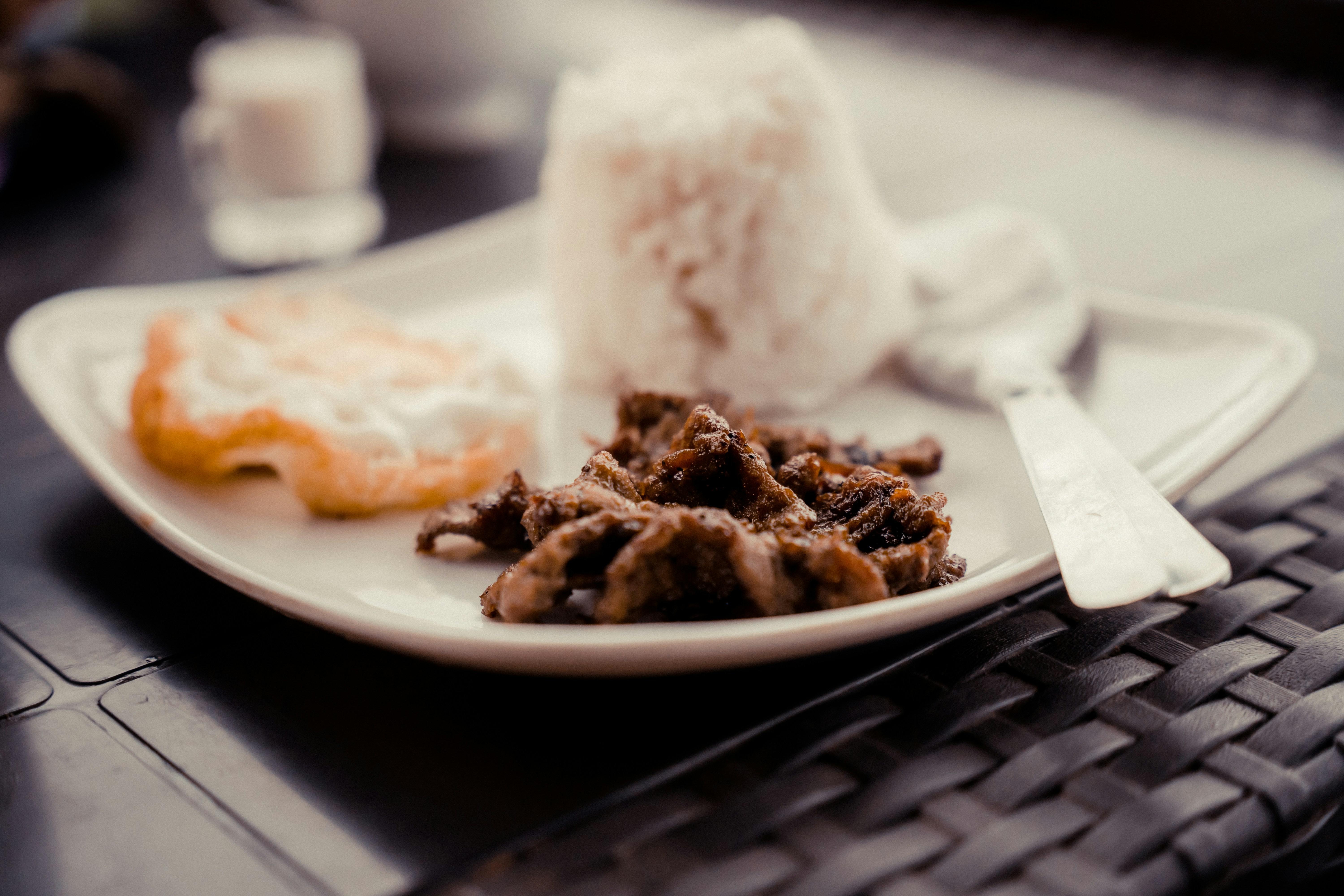 Charred Bits, Quiet Light: Plate of Meat and Rice on a Woven Table