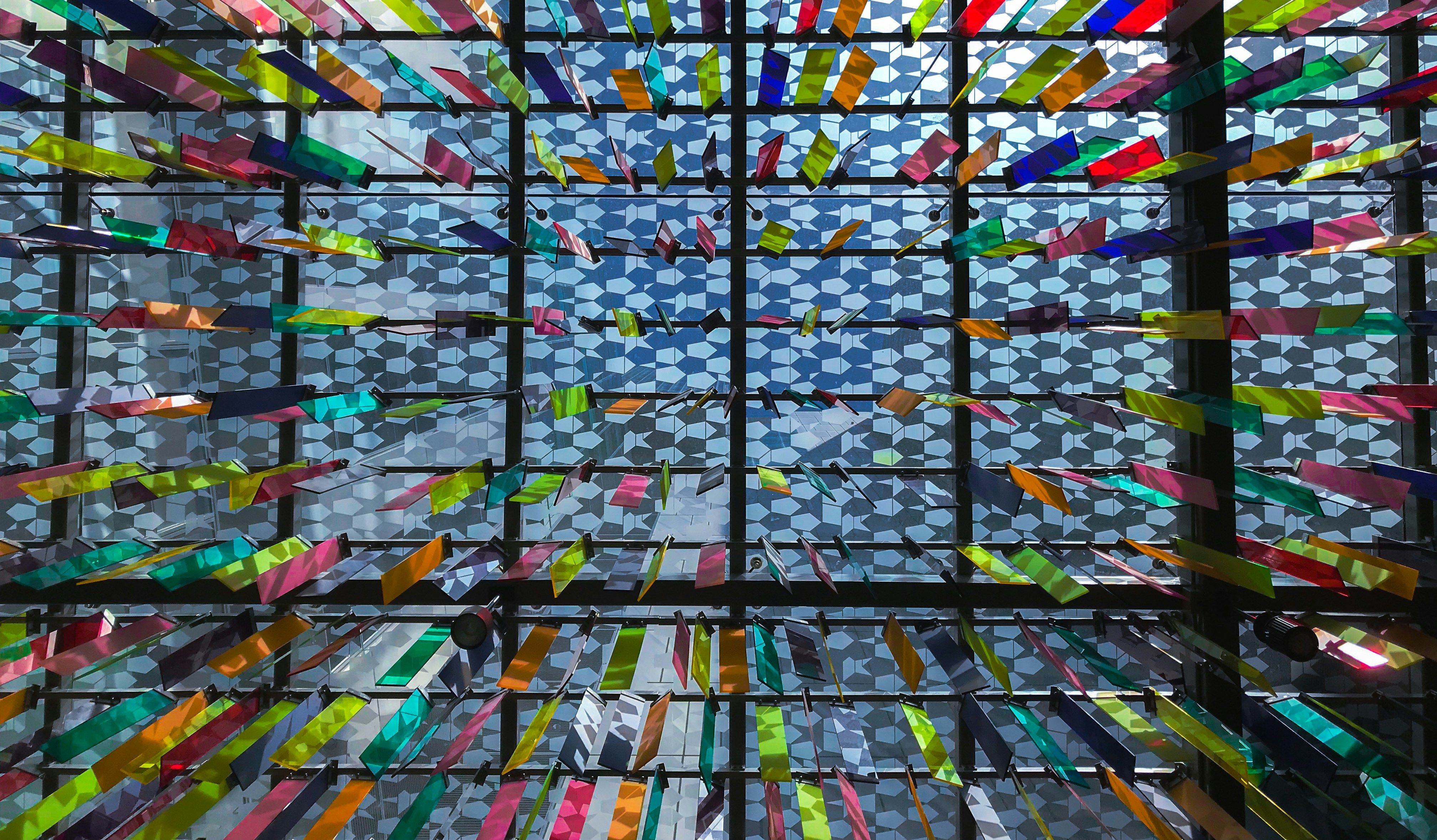 Colorful translucent panels suspended in a geometric grid against a patterned glass ceiling.