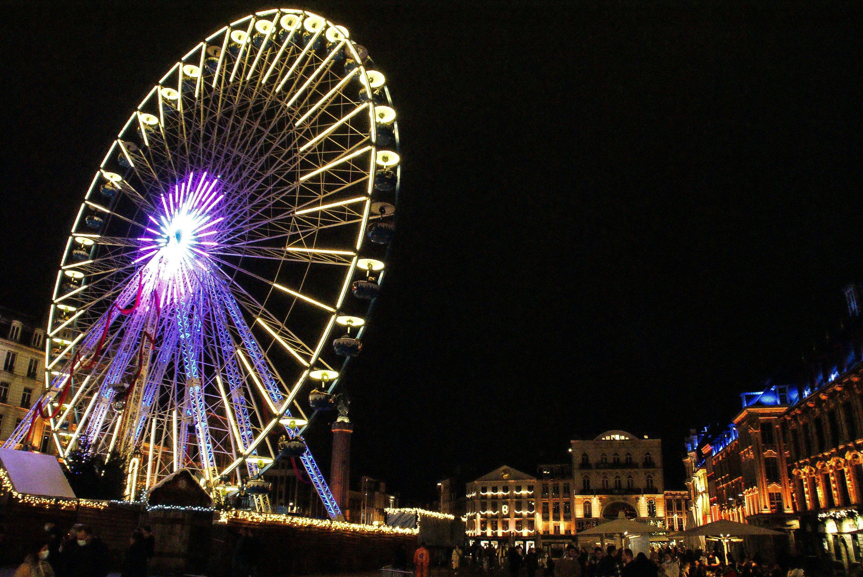 Giant Ferris wheel glowing with colorful lights beside historic buildings at night.