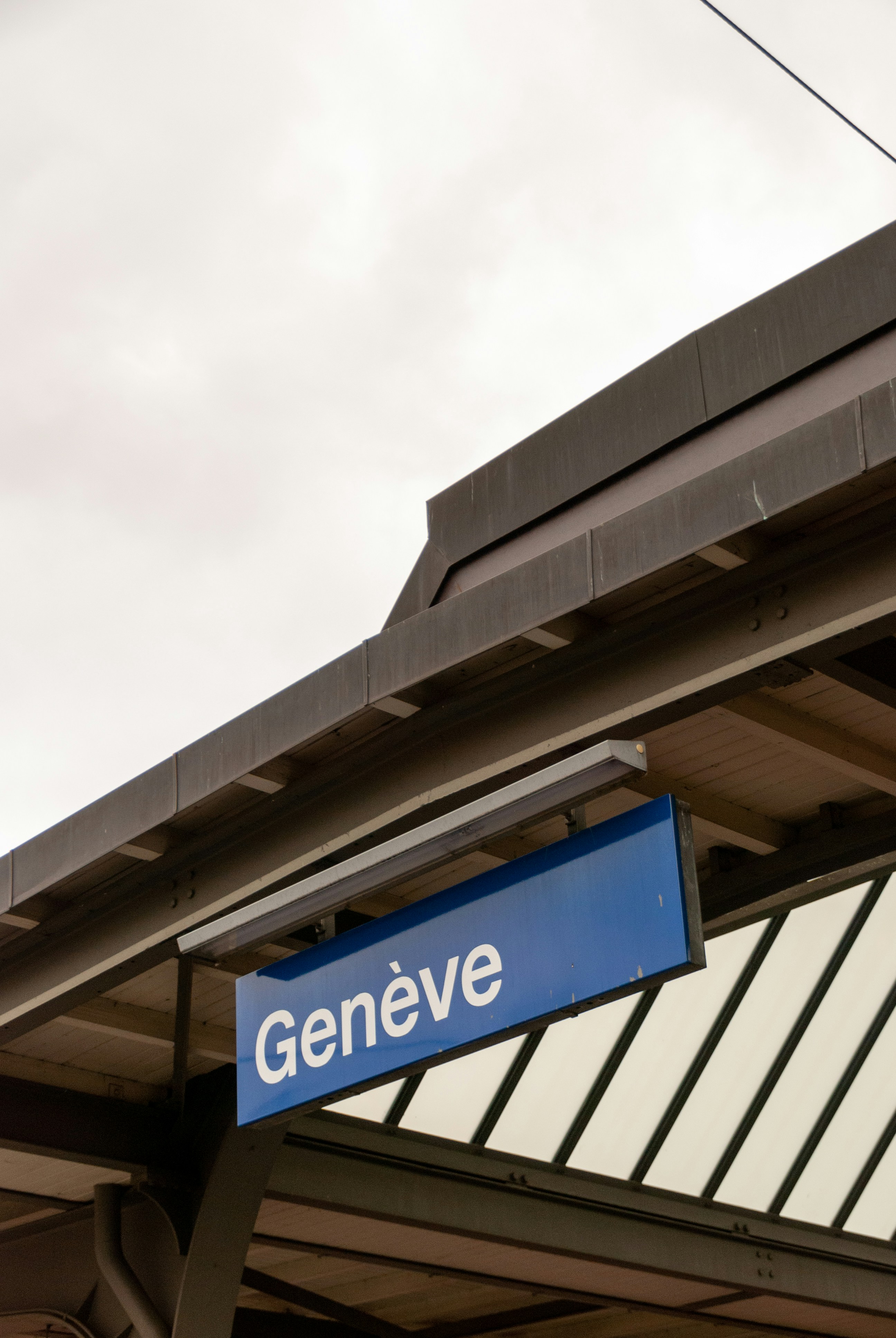 Under the Canopy: Genève Station Sign Framed by Industrial Angles