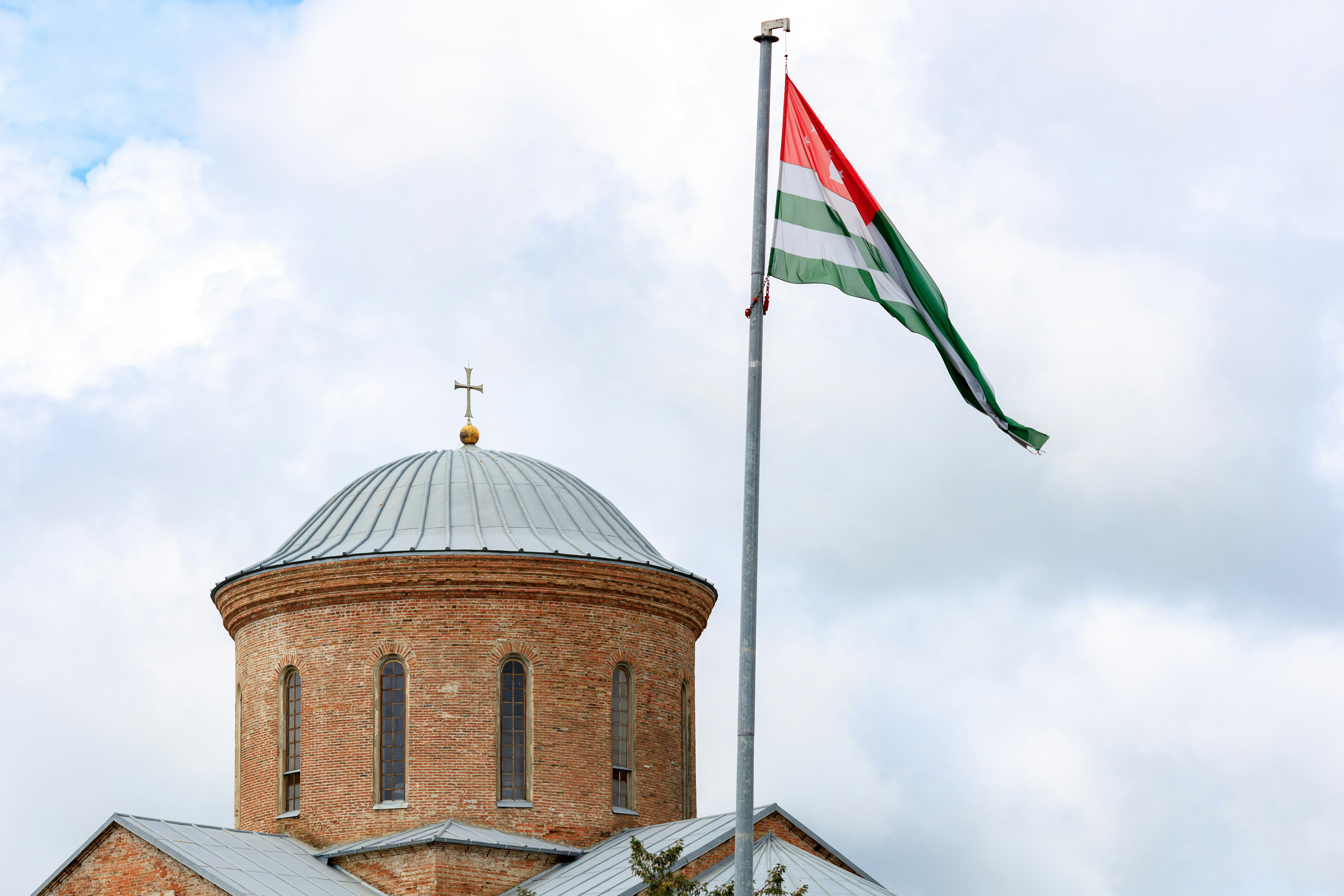 Hungarian flag waving proudly next to a historic church dome under a cloudy sky.