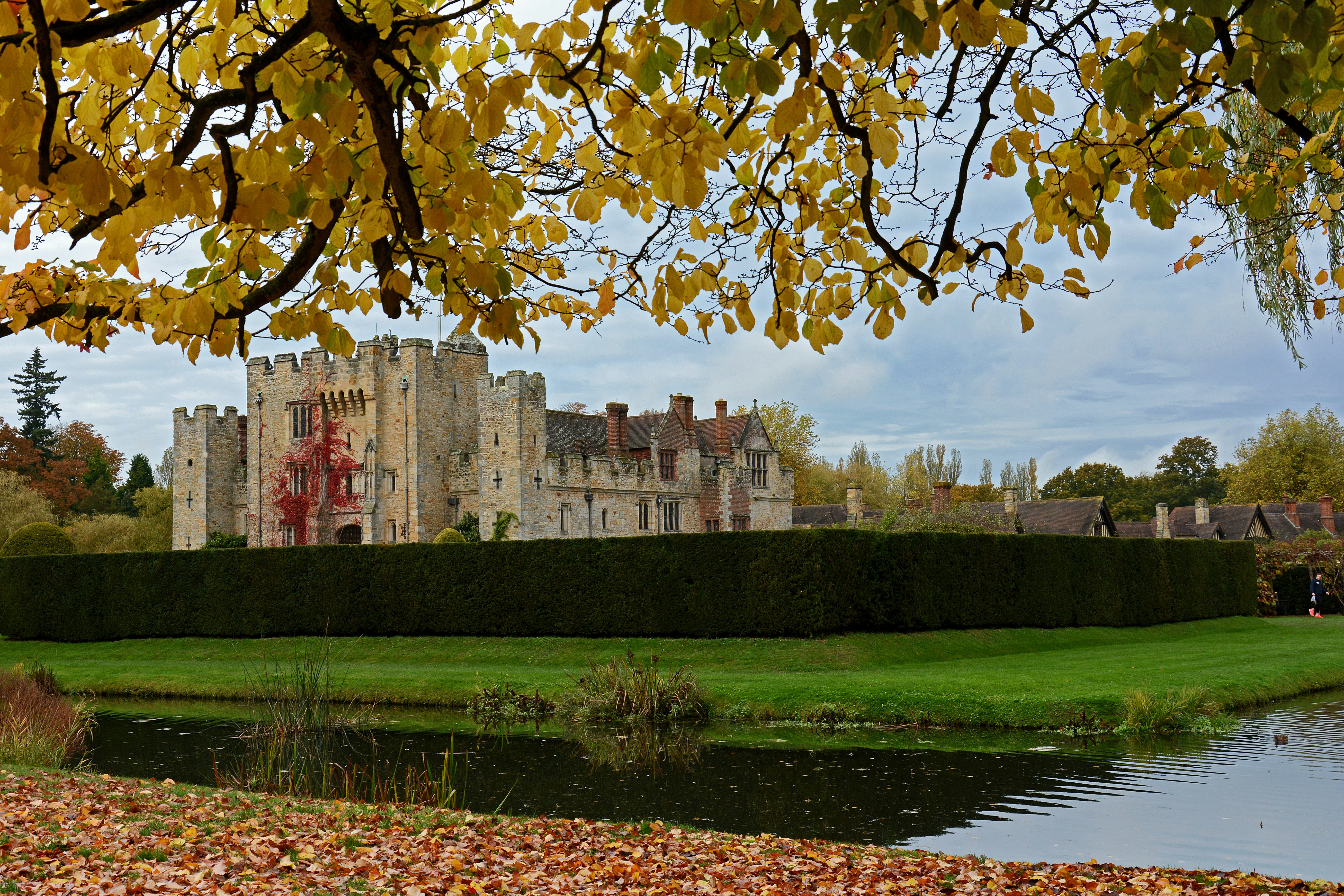 Historic castle surrounded by vibrant autumn foliage and a serene pond, showcasing seasonal beauty and architectural grandeur.