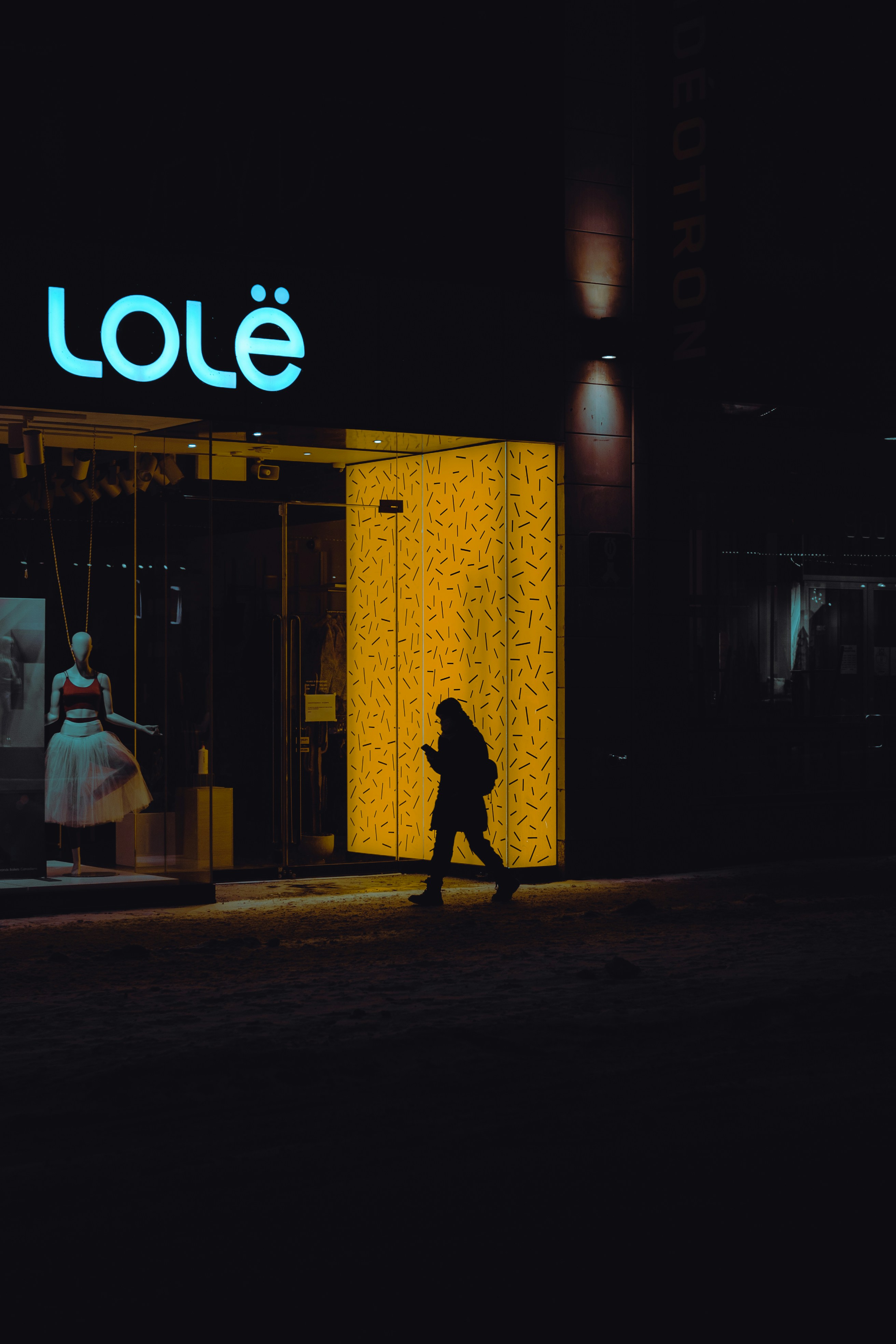 Neon Quiet: A Silhouette Walks Past a Glowing Boutique