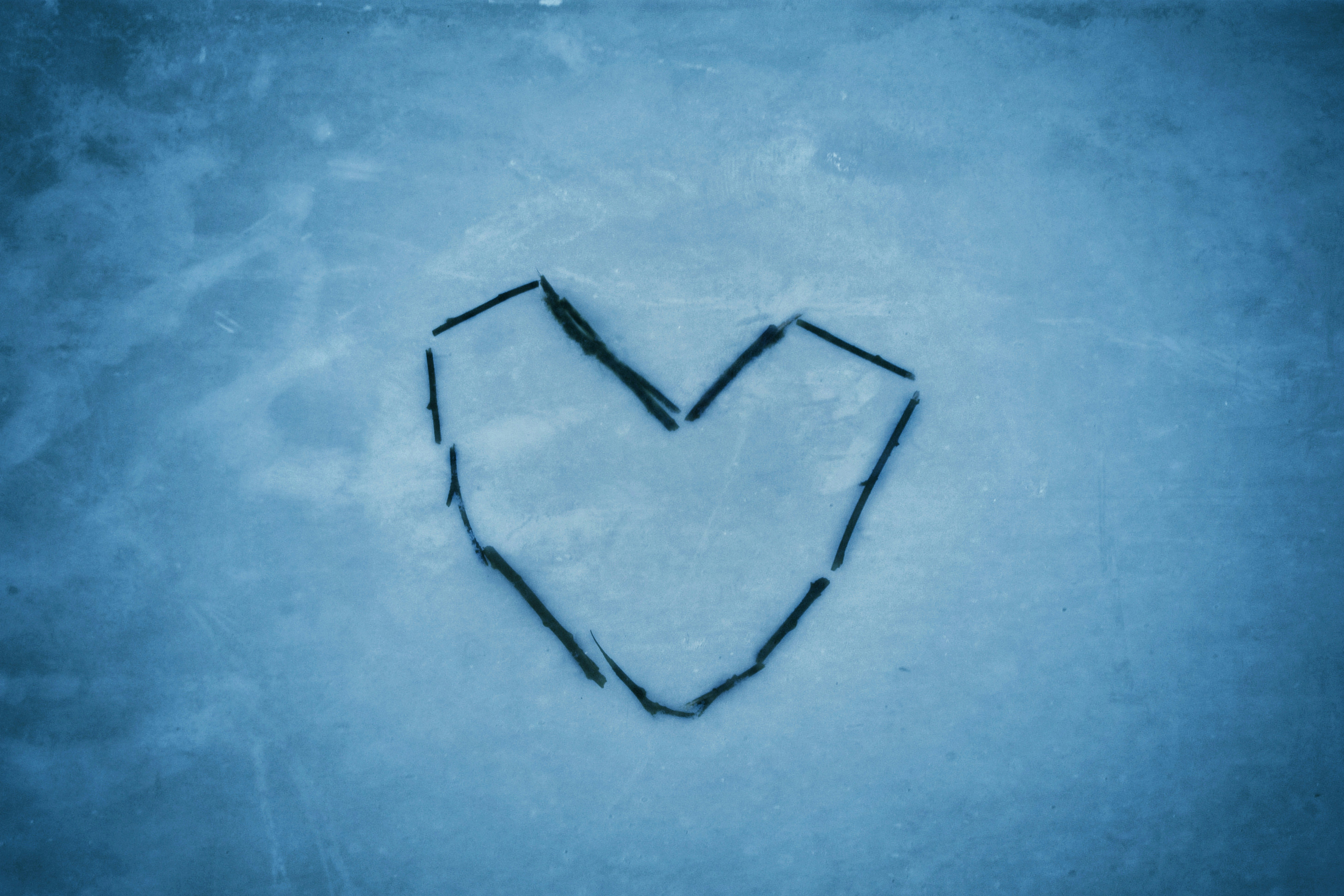 A heart shape crafted from sticks is etched into a smooth, icy surface, evoking a sense of winter romance.