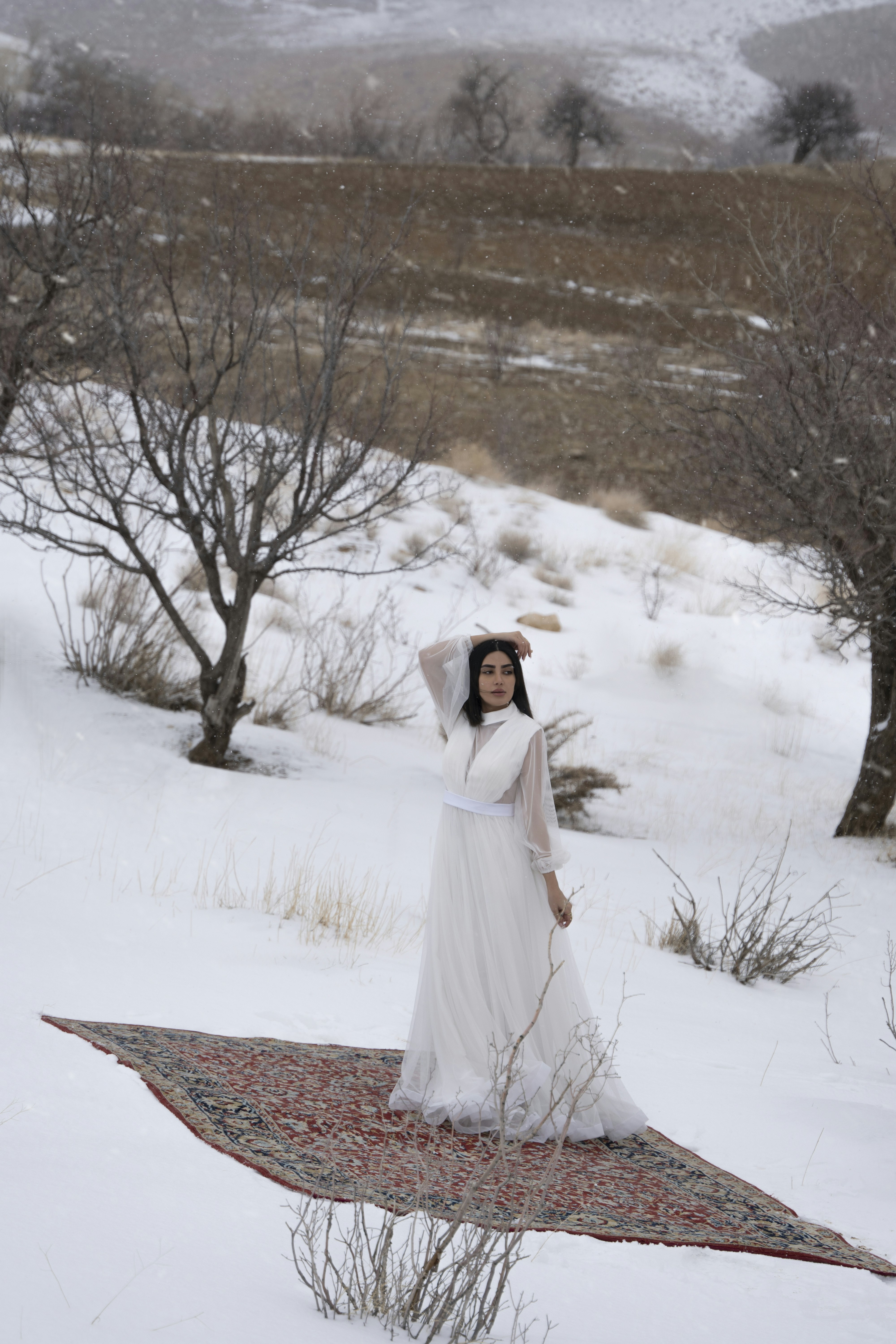 White-gowned figure on a snow-carpeted hillside, mid-pose under bare branches