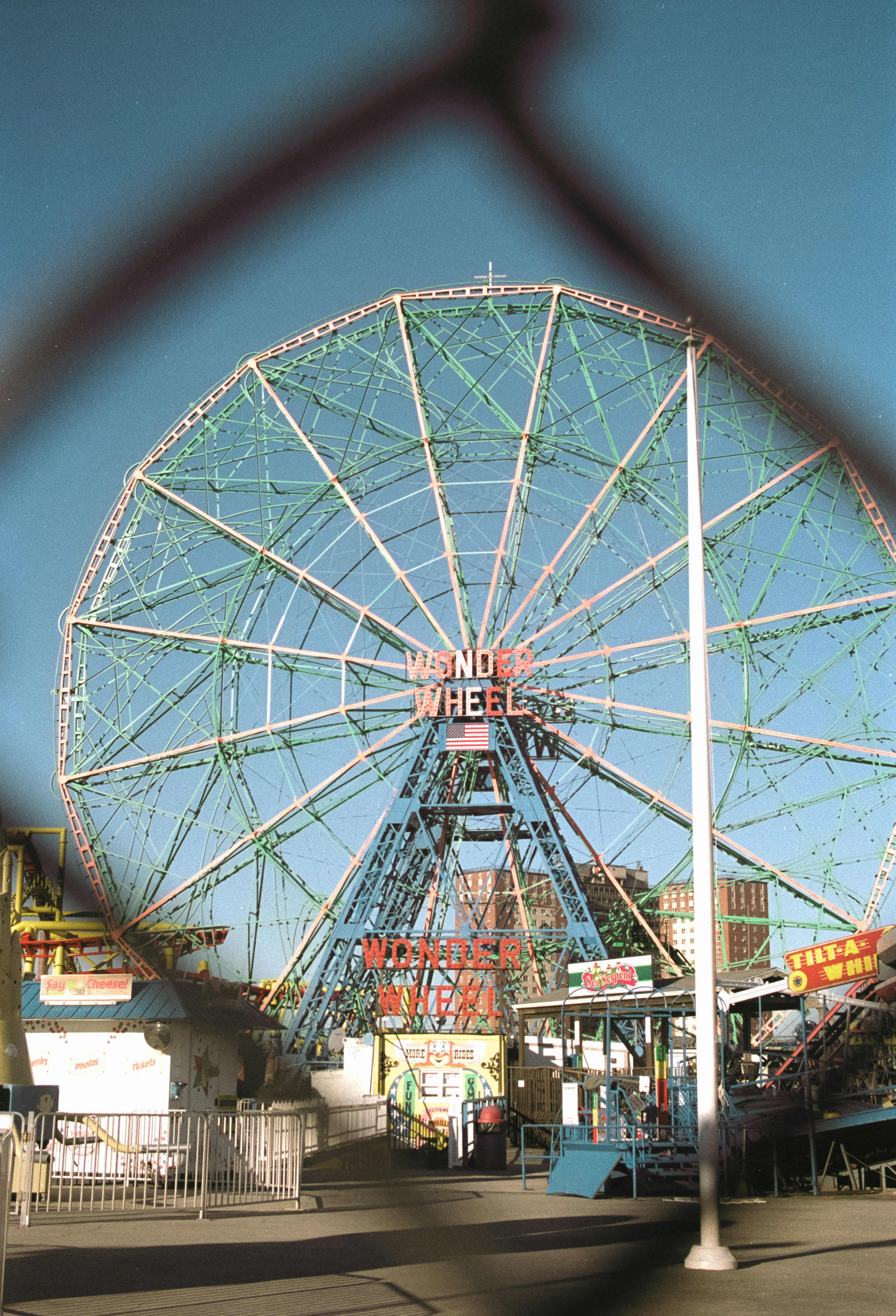The Wonder Wheel, a classic amusement park ride, stands tall against a clear blue sky, framed by a chain-link fence. Its vibrant colors and structure evoke a sense of nostalgia.