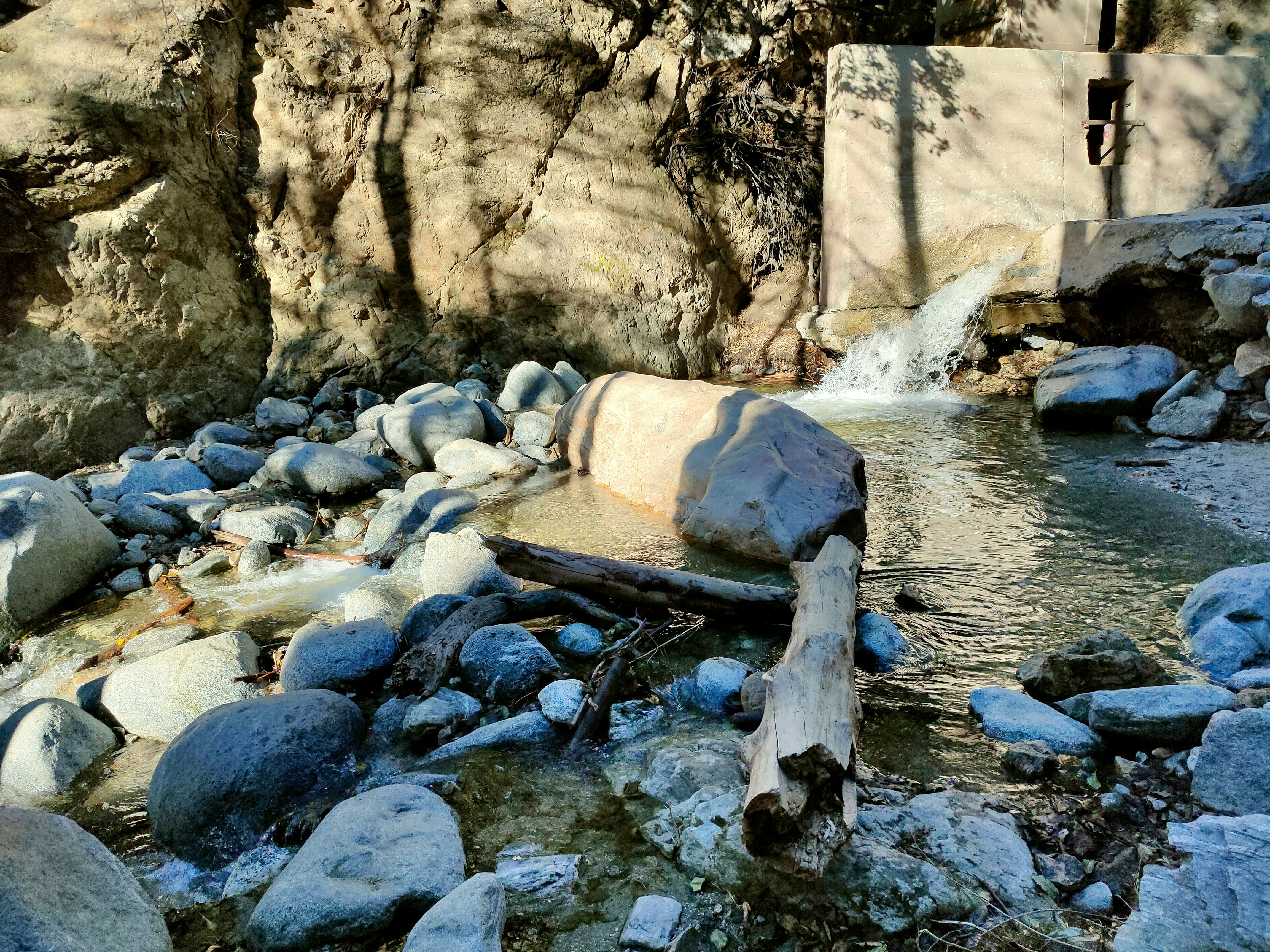 Stream flowing over rocks with sunlight casting shadows on a rocky hillside.