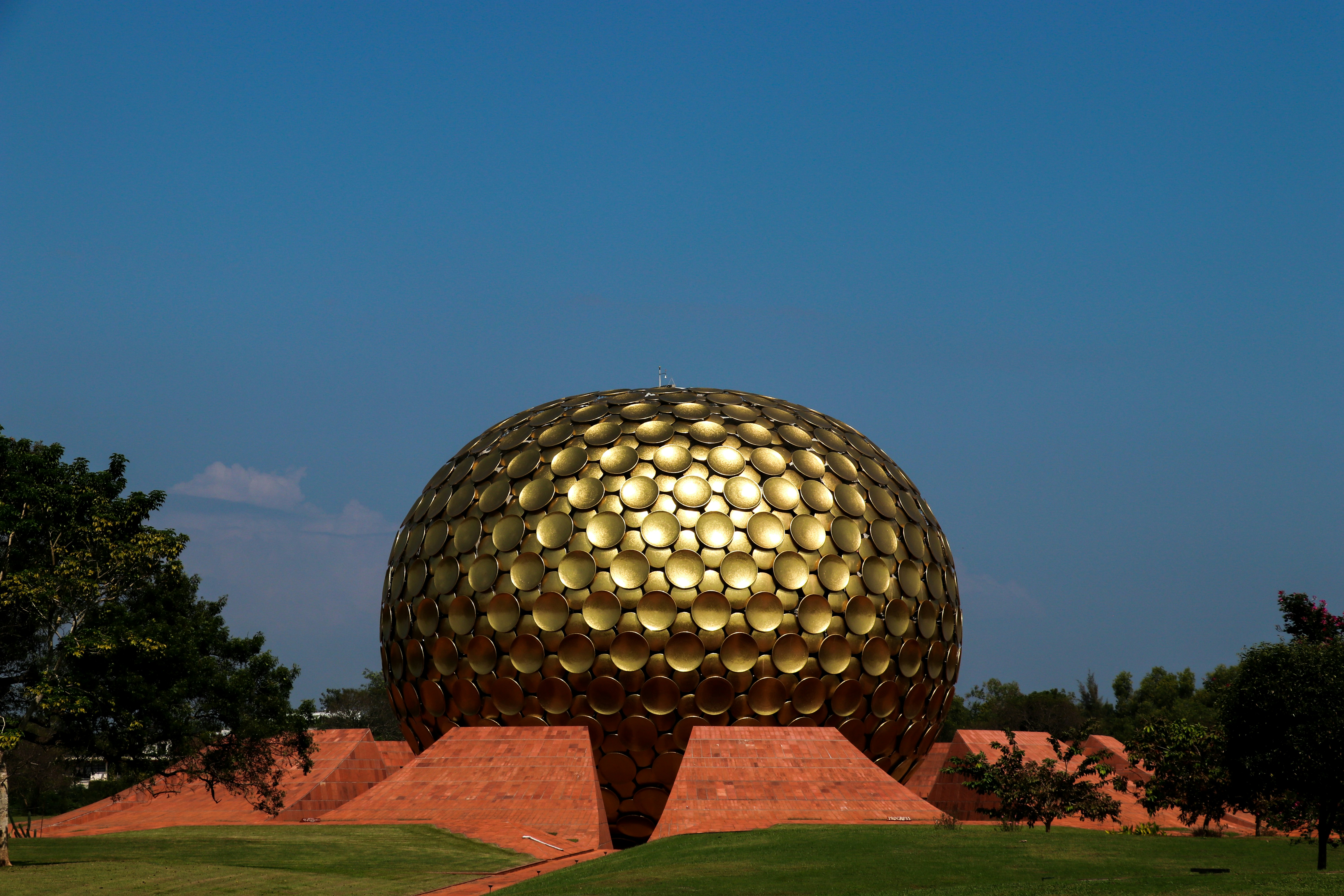 Golden dome structure surrounded by lush greenery under a clear blue sky. The design features a unique pattern that reflects light beautifully.