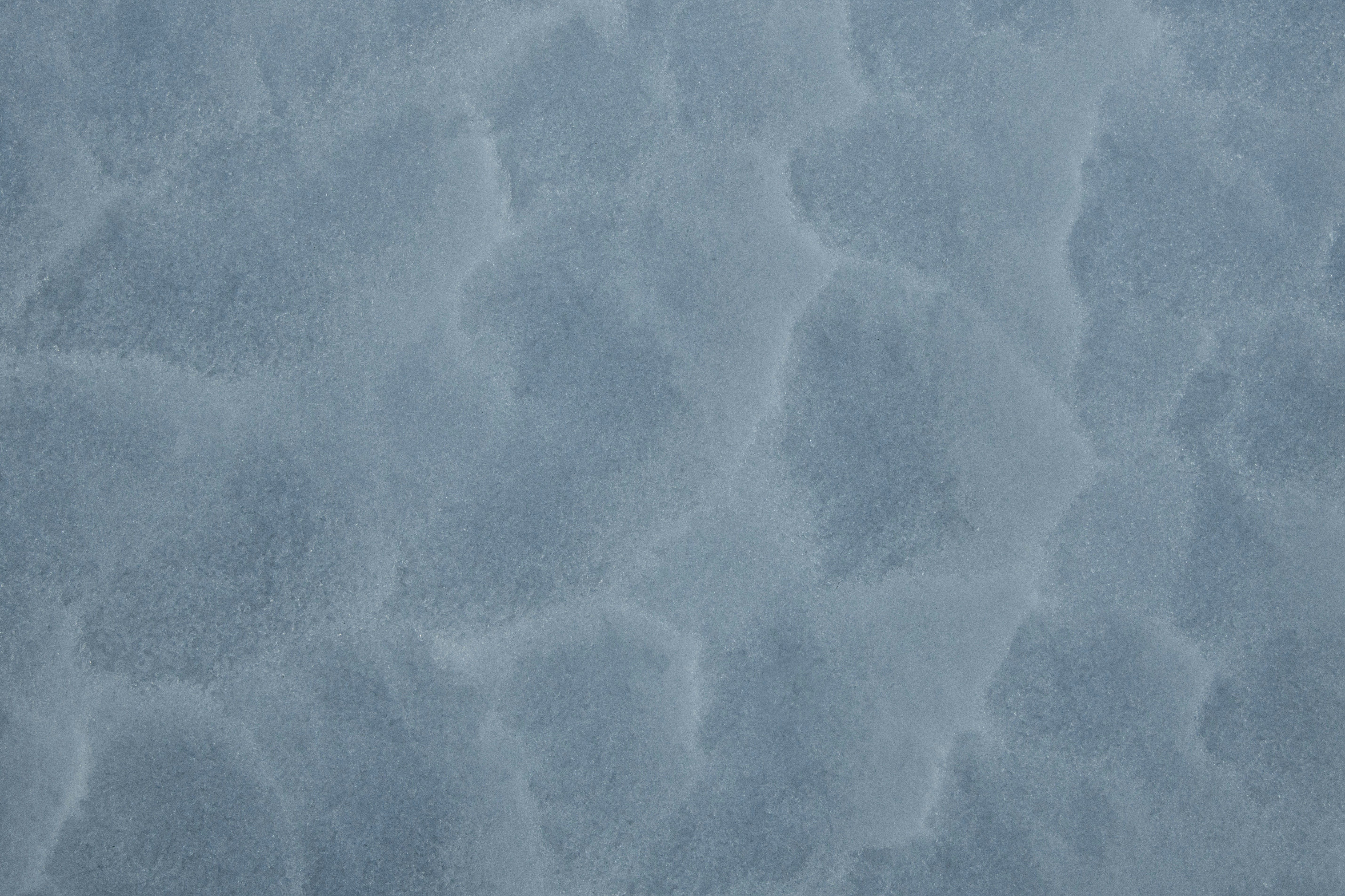 Intricate patterns formed by snow create a textured surface that reflects the cool tones of winter. The composition emphasizes the delicate interplay of light and shadow.