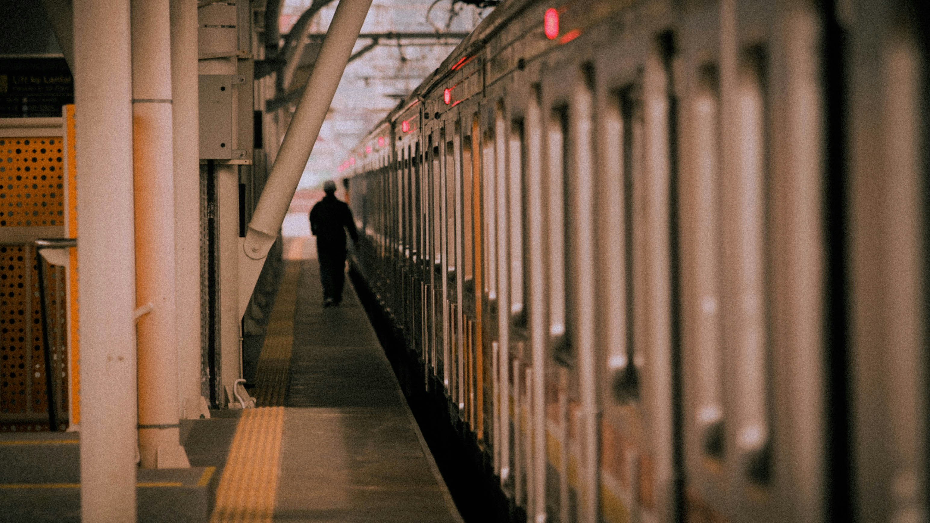 Empty train platform with a lone figure walking beside a stationary train under soft lighting.