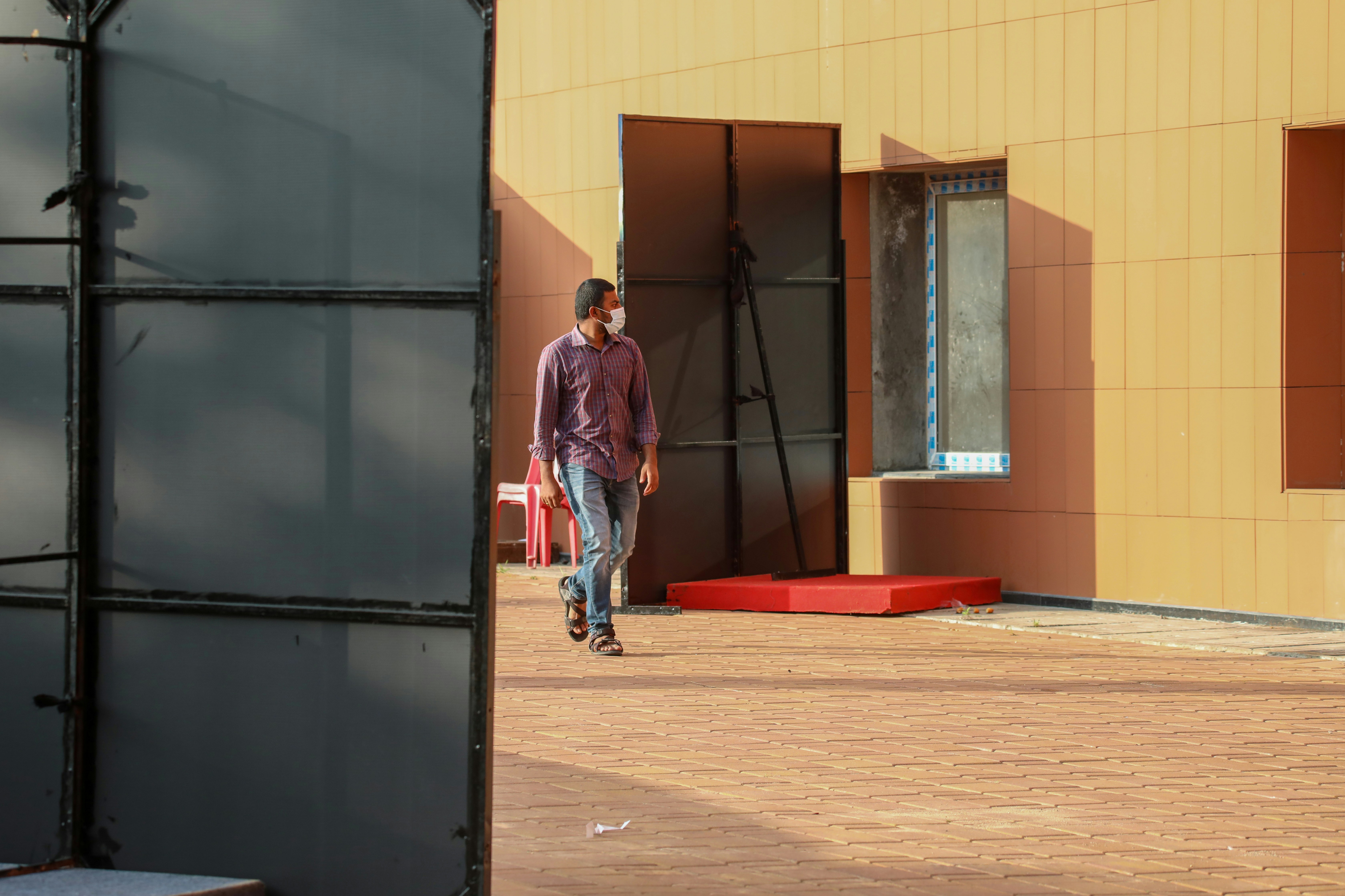 Mask-Wearing Walker Tracing a Path Through a Sunlit Yellow Courtyard