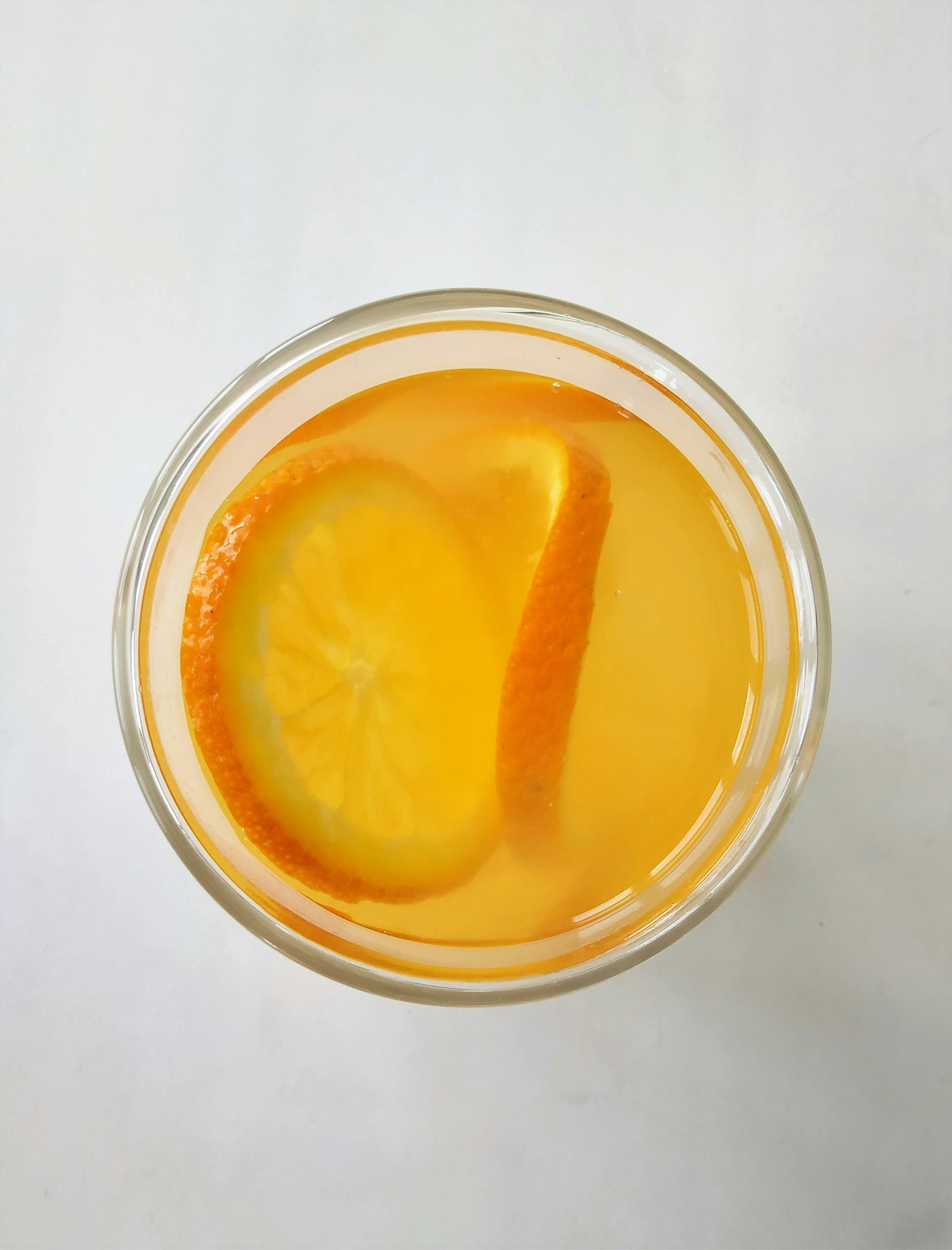 A glass filled with vibrant orange juice and two slices of orange floating on top, set against a clean white background.