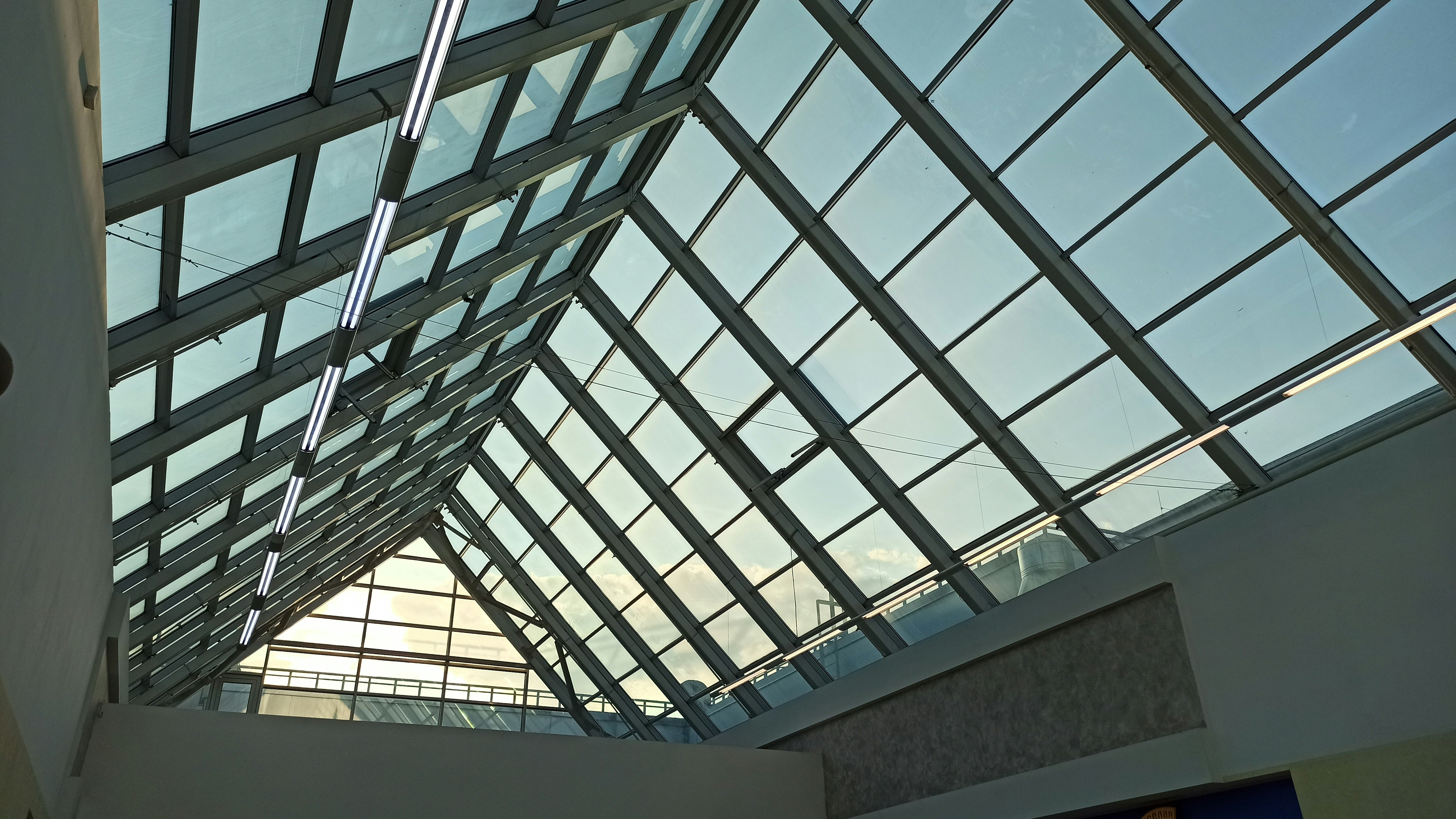 Geometric glass ceiling reflecting the soft hues of the sky, showcasing modern architectural design elements.