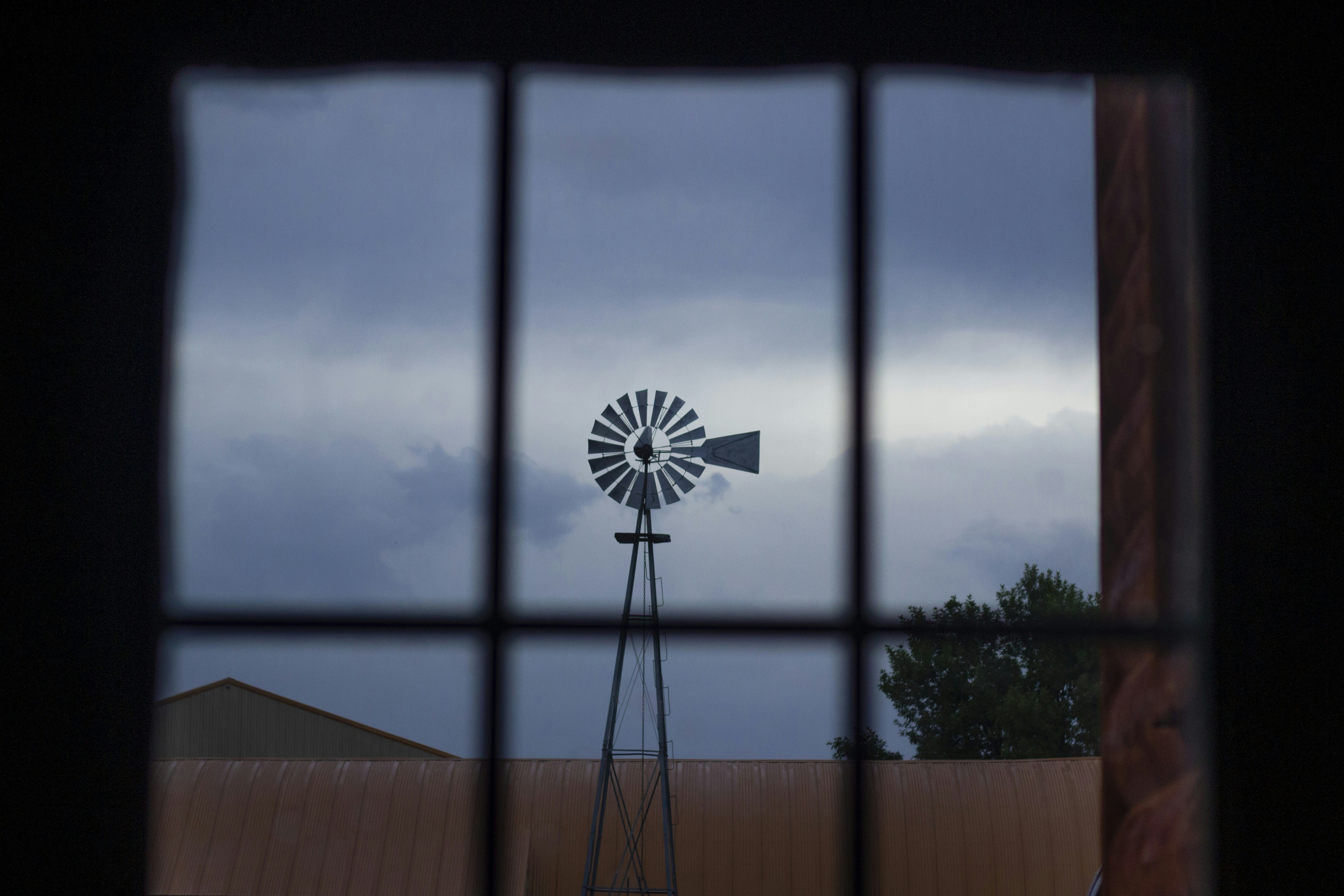 Vintage windmill silhouetted against a stormy sky, framed by a rustic window. The scene evokes a sense of nostalgia and tranquility.