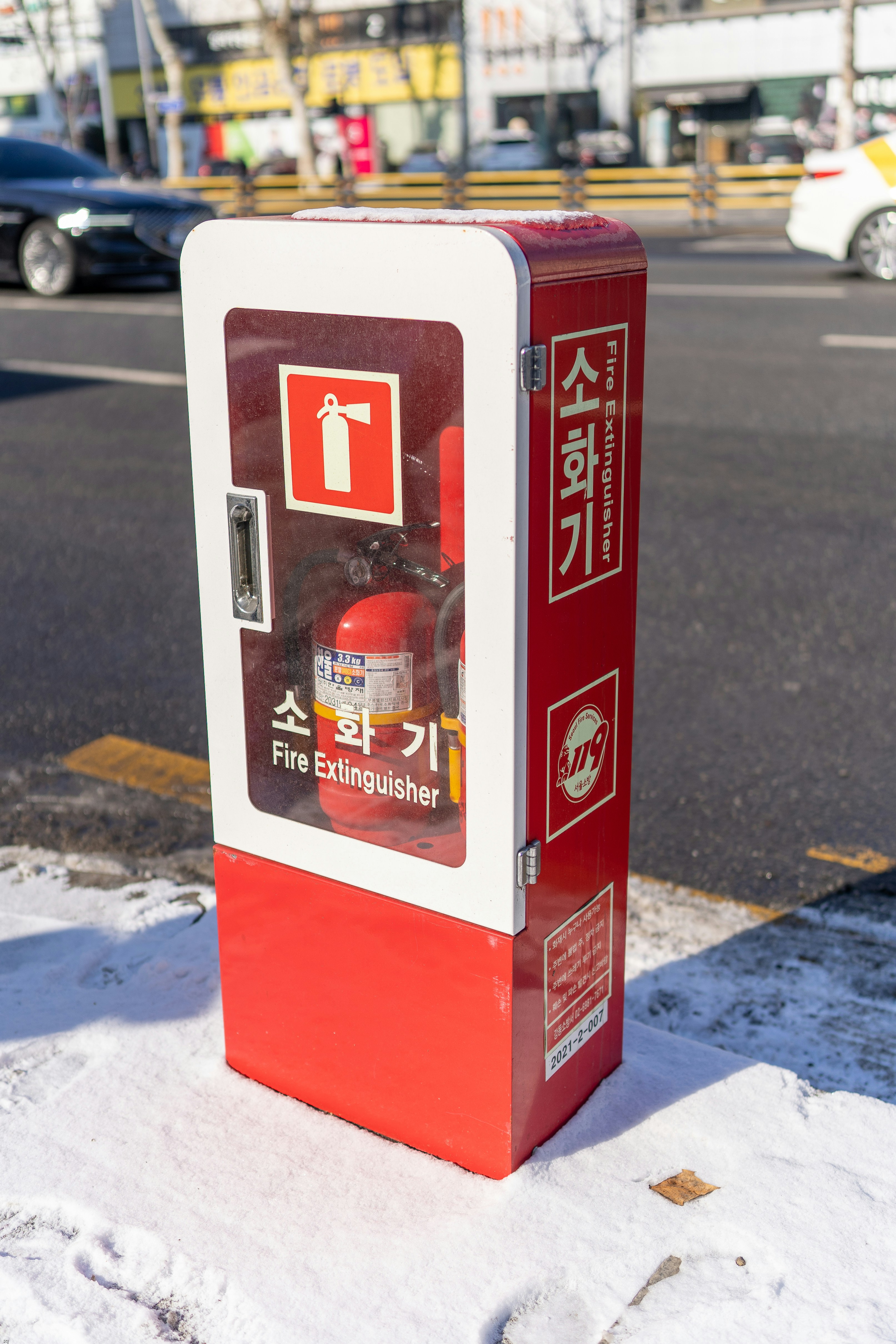 Urban Red Sentinel: Fire Extinguisher Cabinet in Snow on a Busy Street