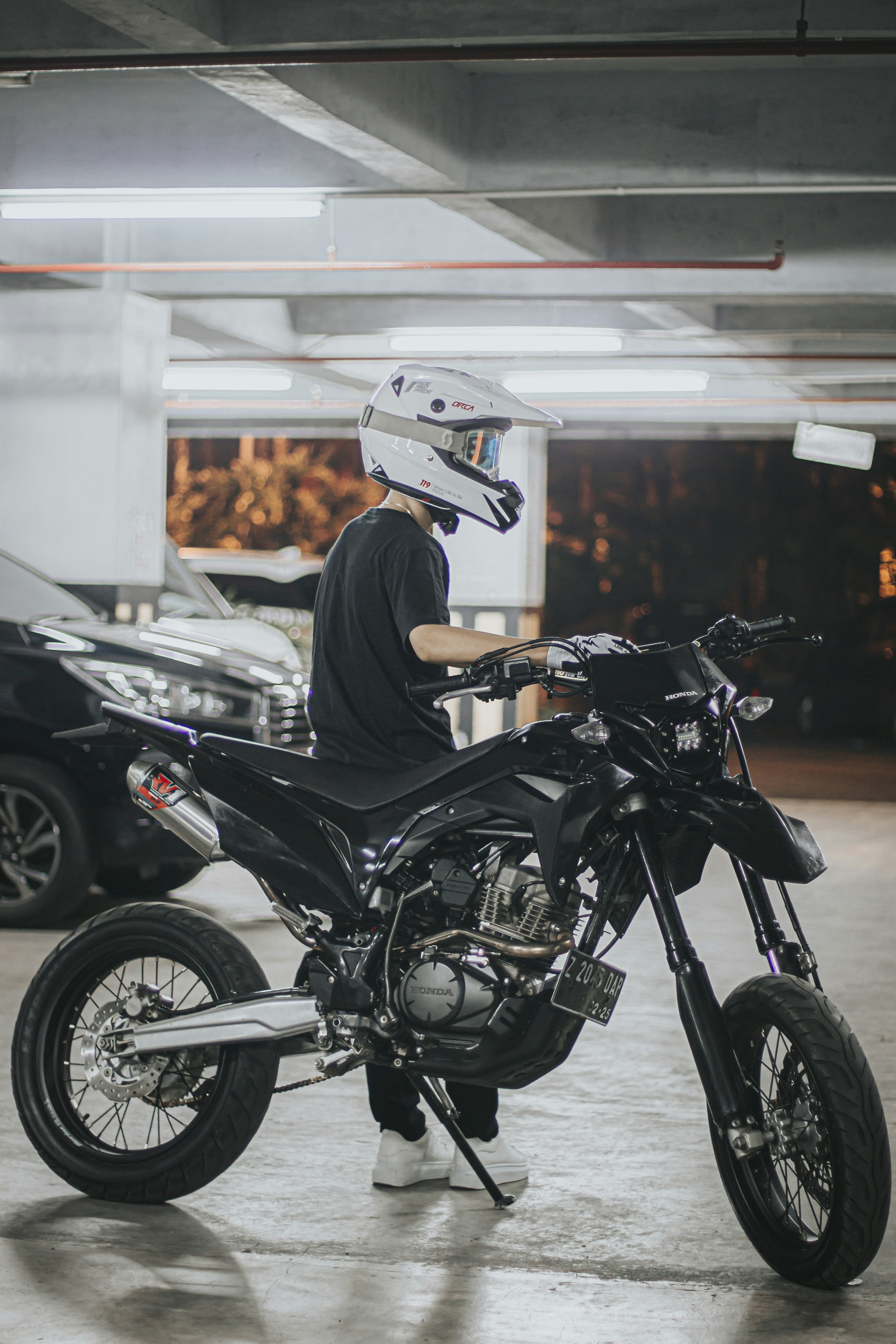 A man sitting on a motorcycle in a parking garage photo – Free Garut ...