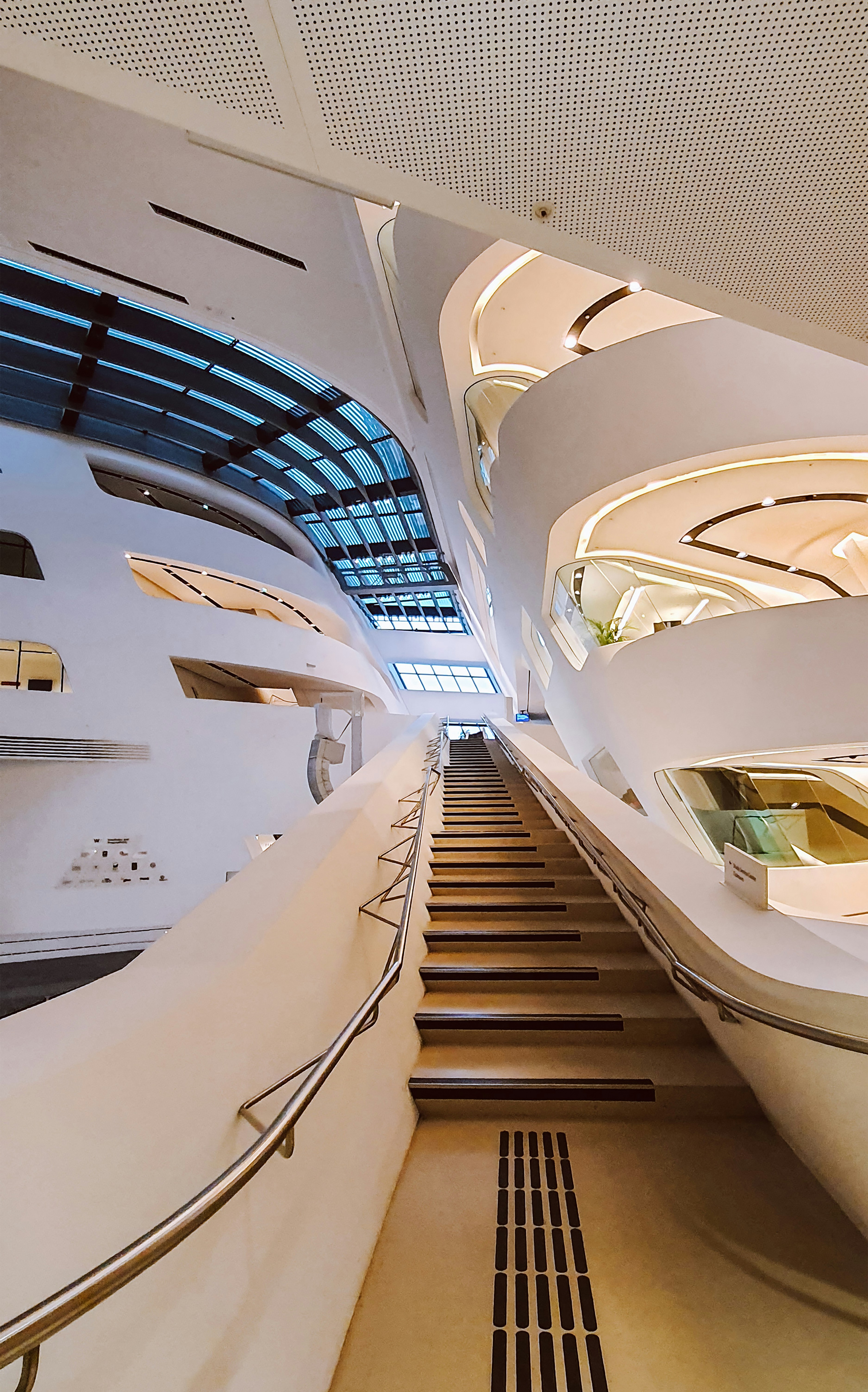 Curved staircase leading through a modern architectural interior with sleek lines and dynamic lighting.