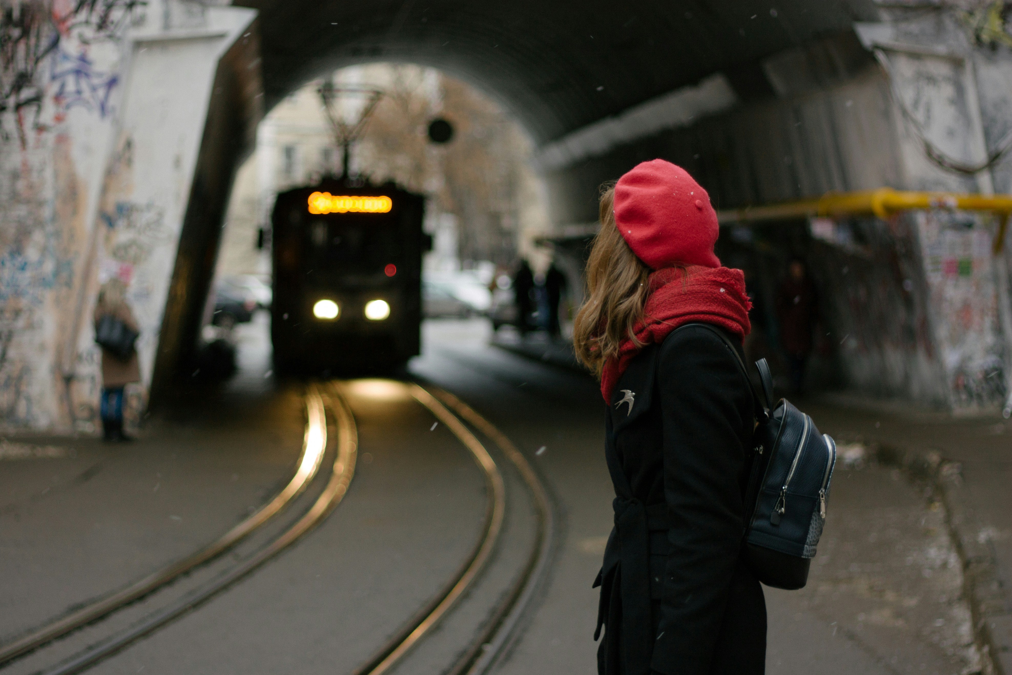 Scarlet-Hooded Figure in a Graffiti Tunnel as a Tram Approaches