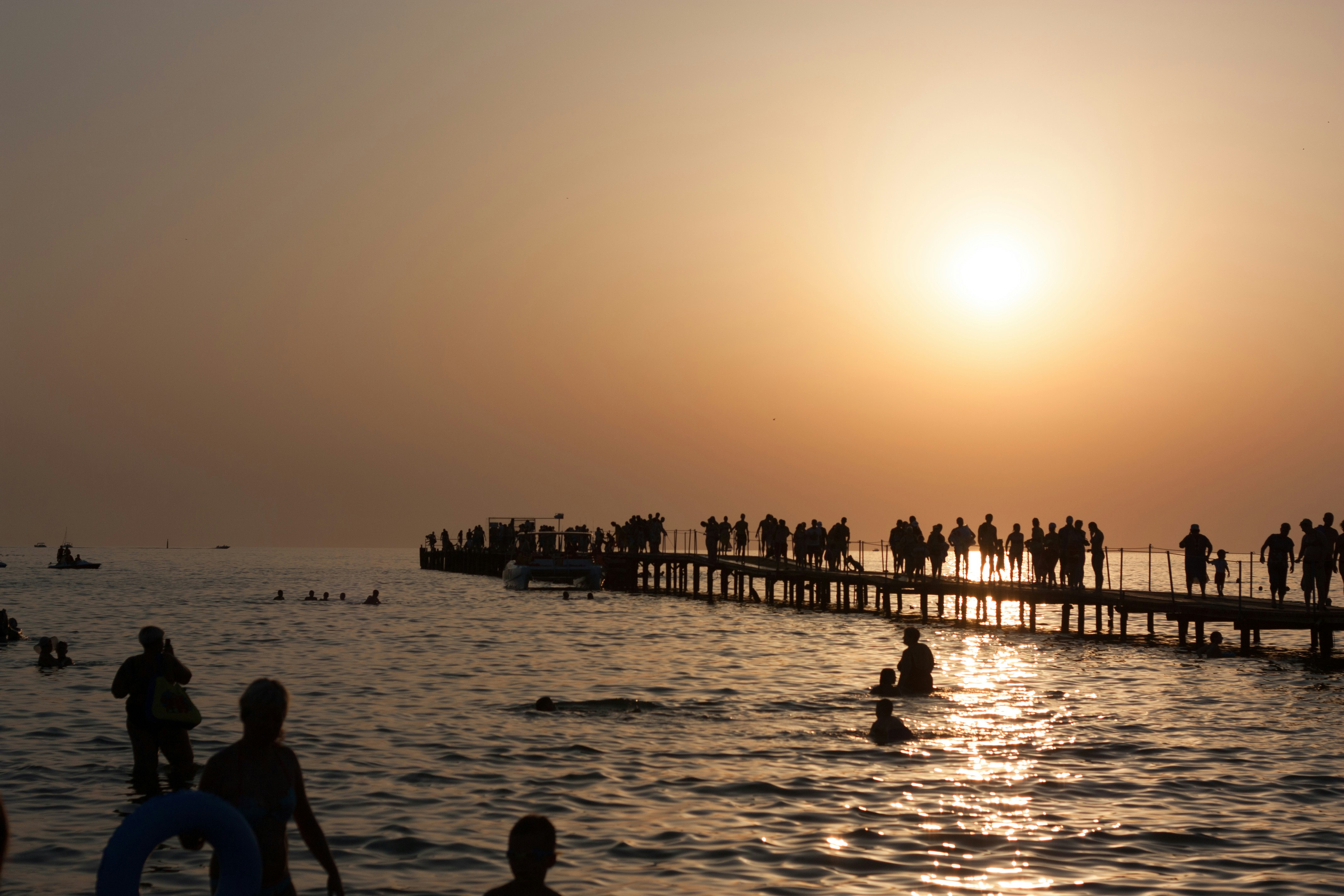 Sunlit Pier of People: Evening Silhouettes Over Calm Sea