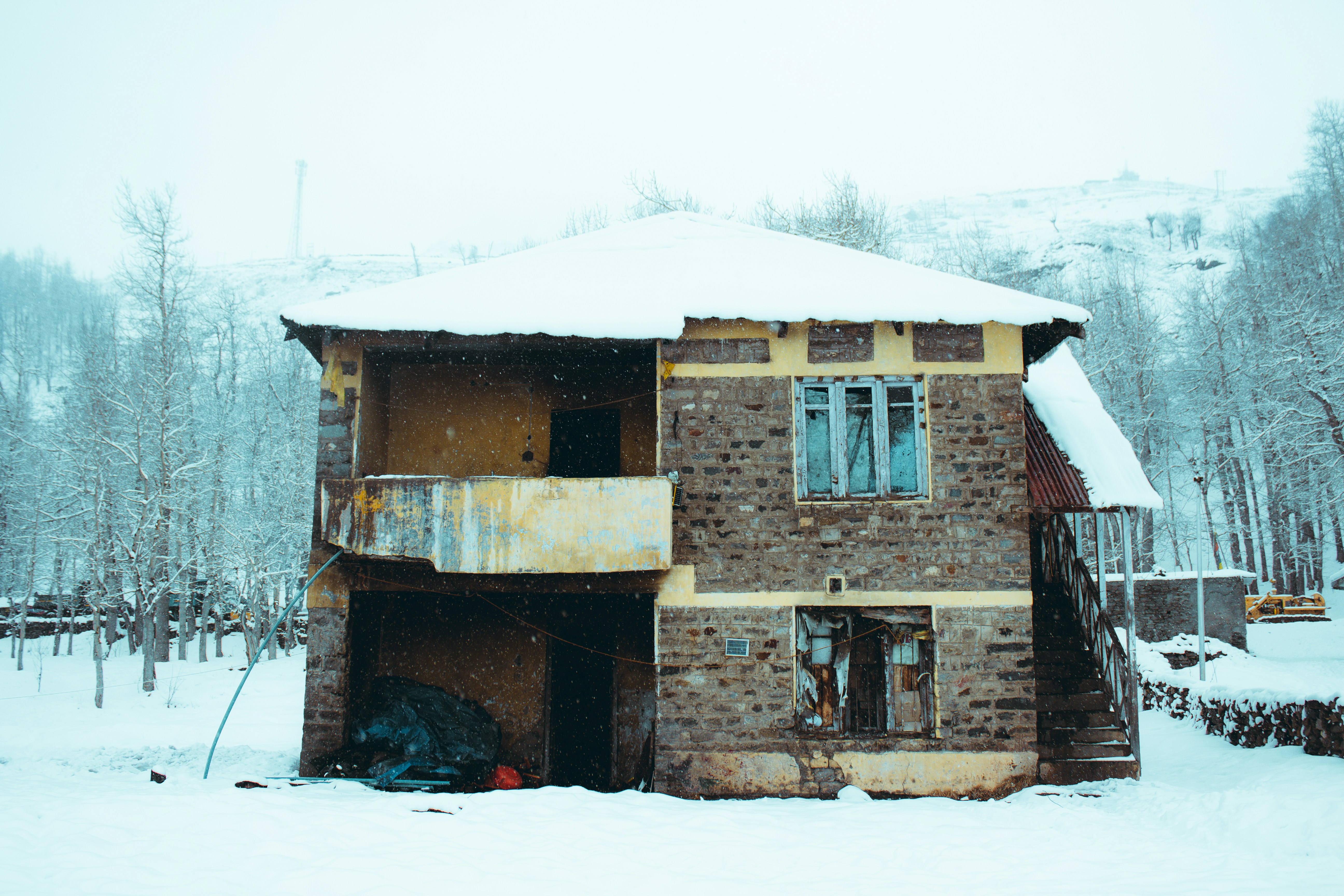 Abandoned stone house blanketed in snow, surrounded by bare trees in a wintry landscape.