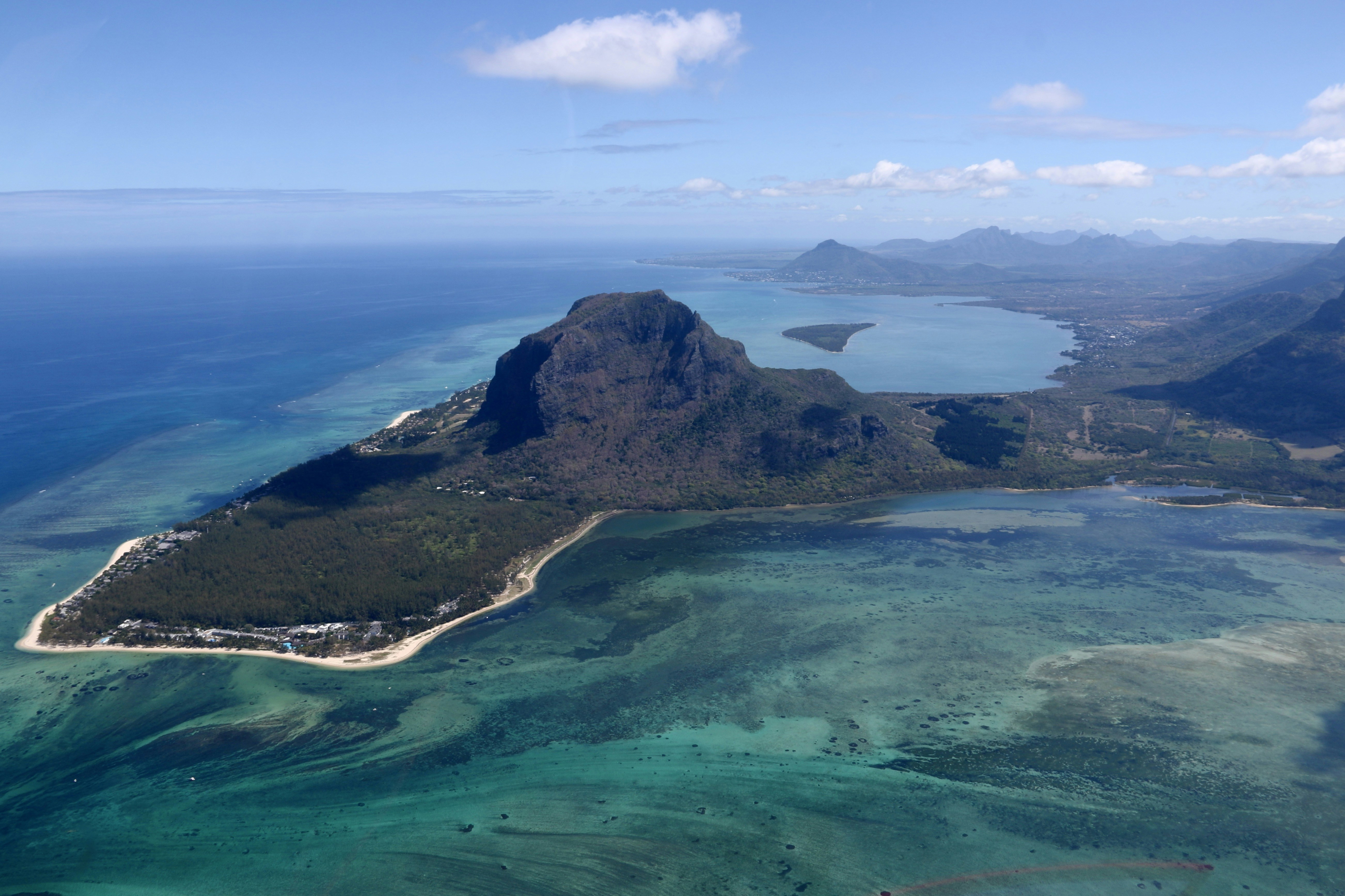 Aerial view of a lush island surrounded by vibrant turquoise waters and coral reefs, showcasing the natural beauty of the coastline.