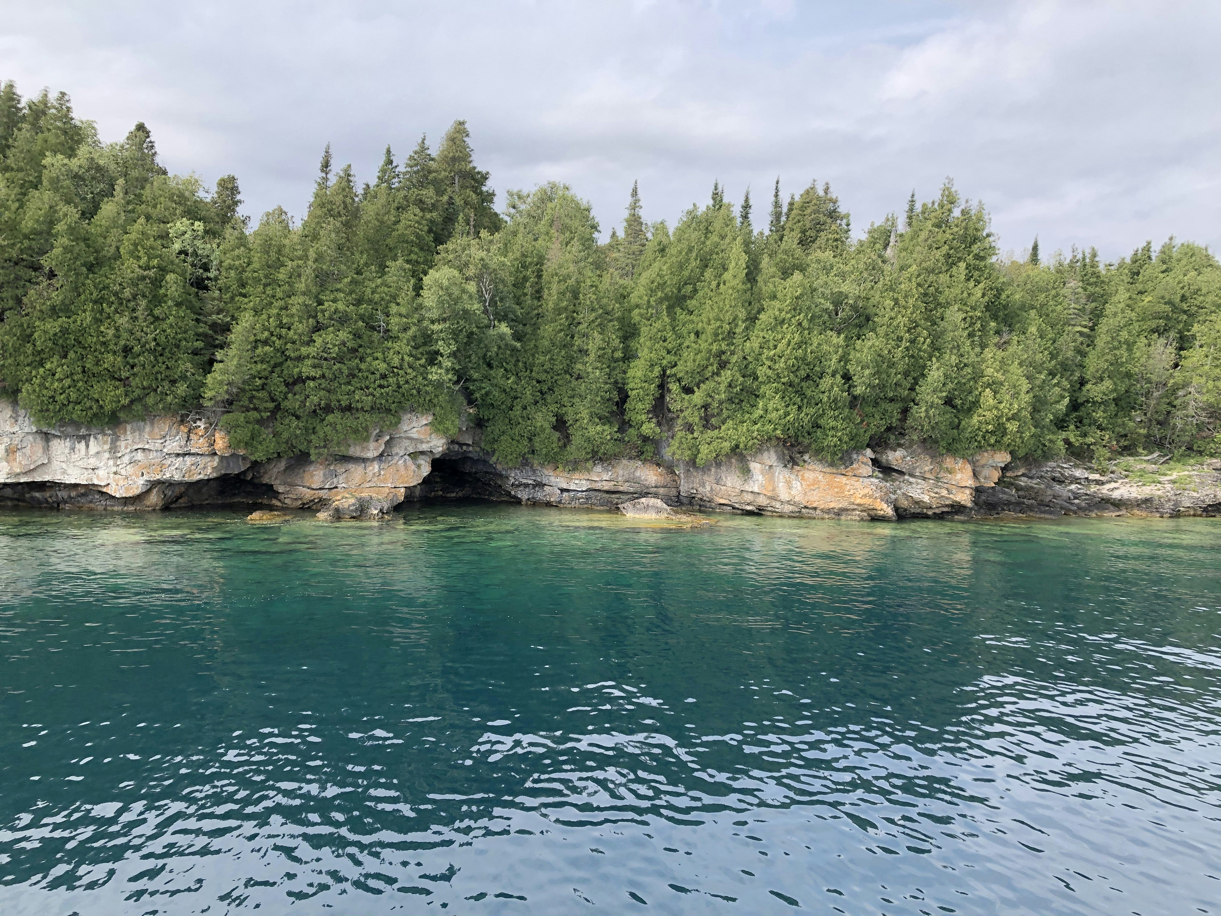 Lush green trees line the rugged shoreline, reflecting in the clear, emerald waters of the lake. The rocky cliffs create a serene natural landscape.