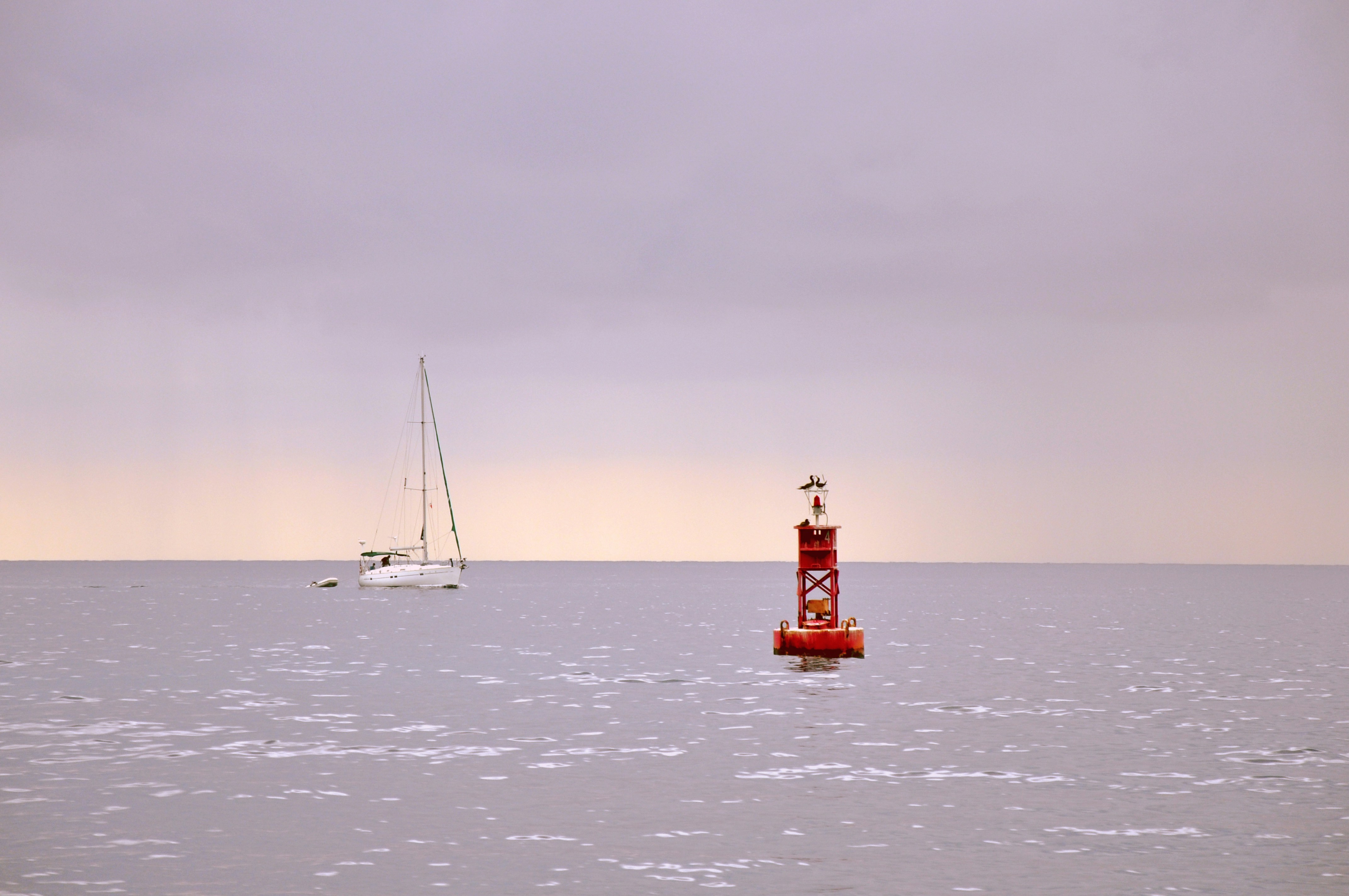 A boat passes mid-horizon beyond a harbor entrance buoy.